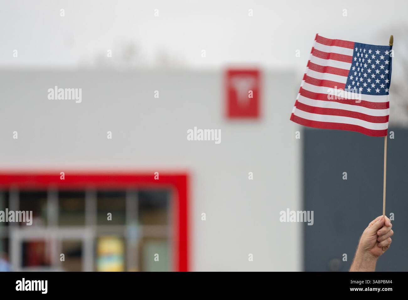 A person holds an American flag with Tesla's Showroom in the background ...