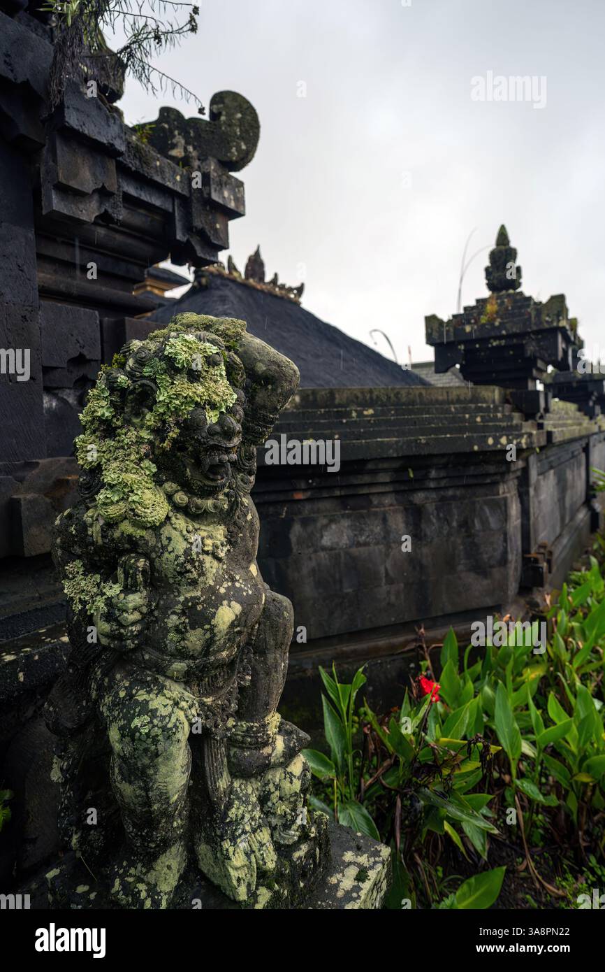A moss-covered stone statue stands at a Balinese temple's entrance ...