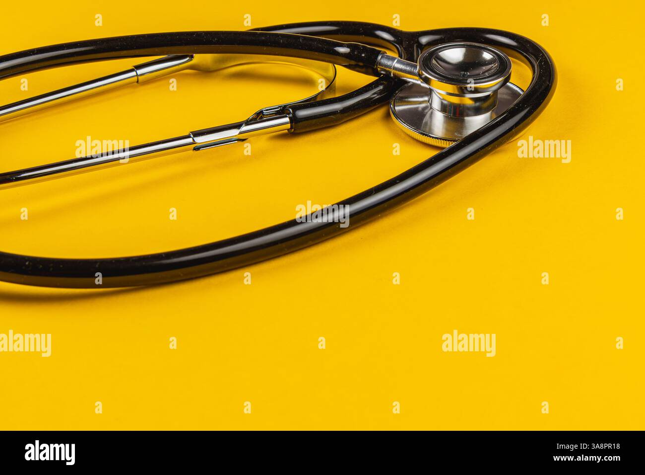 A stethoscope lies on a vibrant yellow surface, highlighting its sleek ...