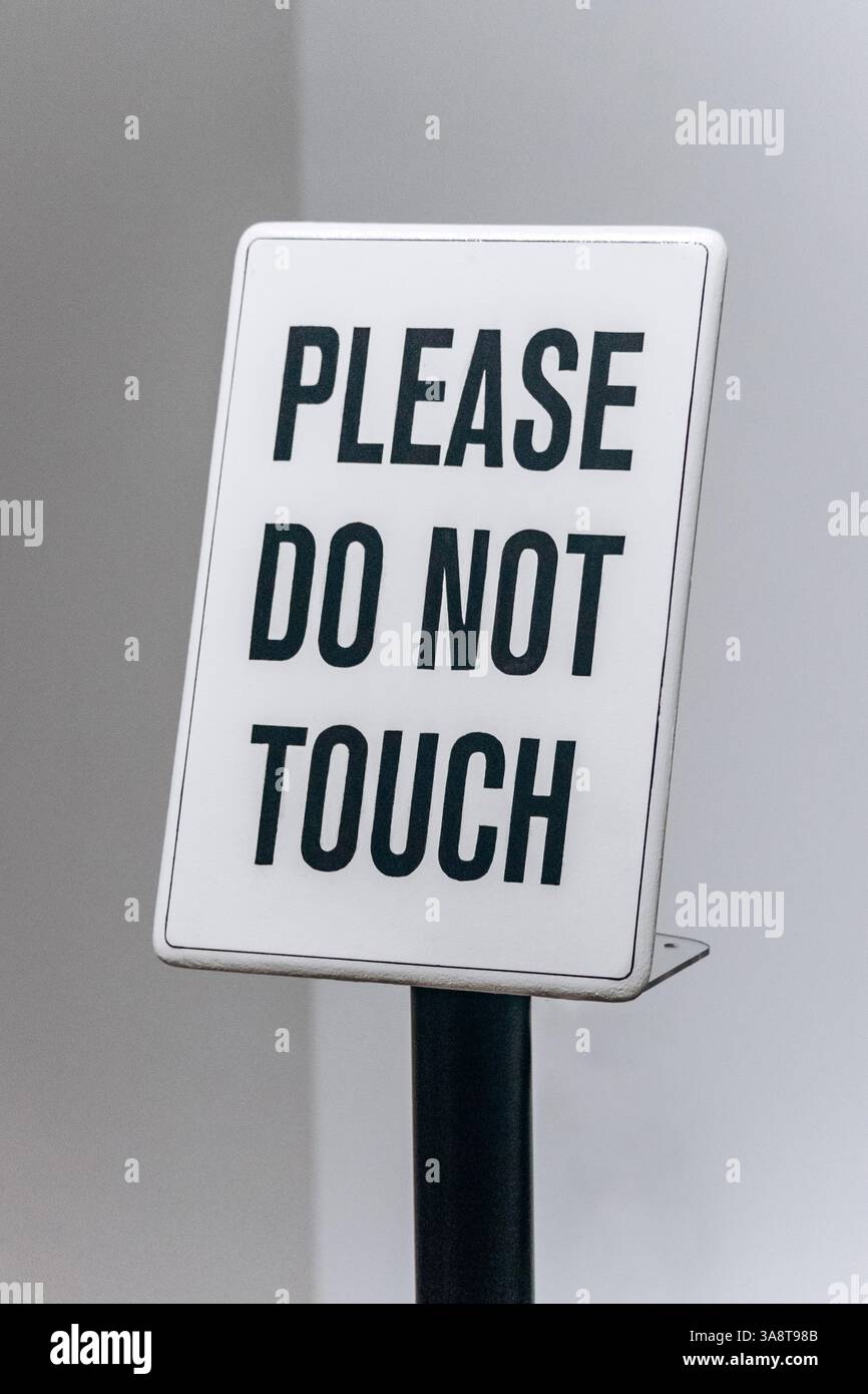 A "Please Do Not Touch" sign displayed on a metal stand, against a ...