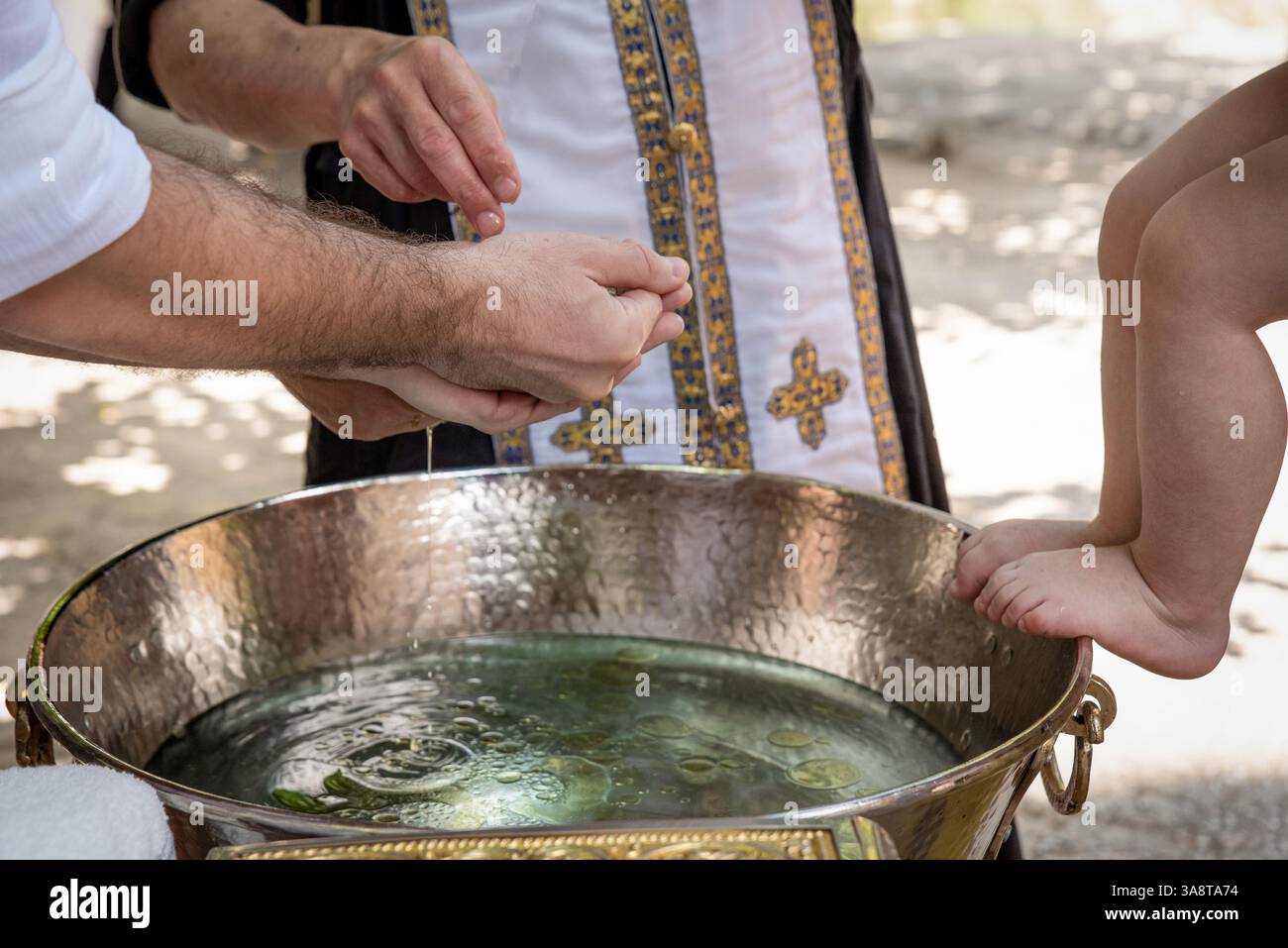 The godfather's hands filled with oil and baby feet stading on the holy font during a greek ...
