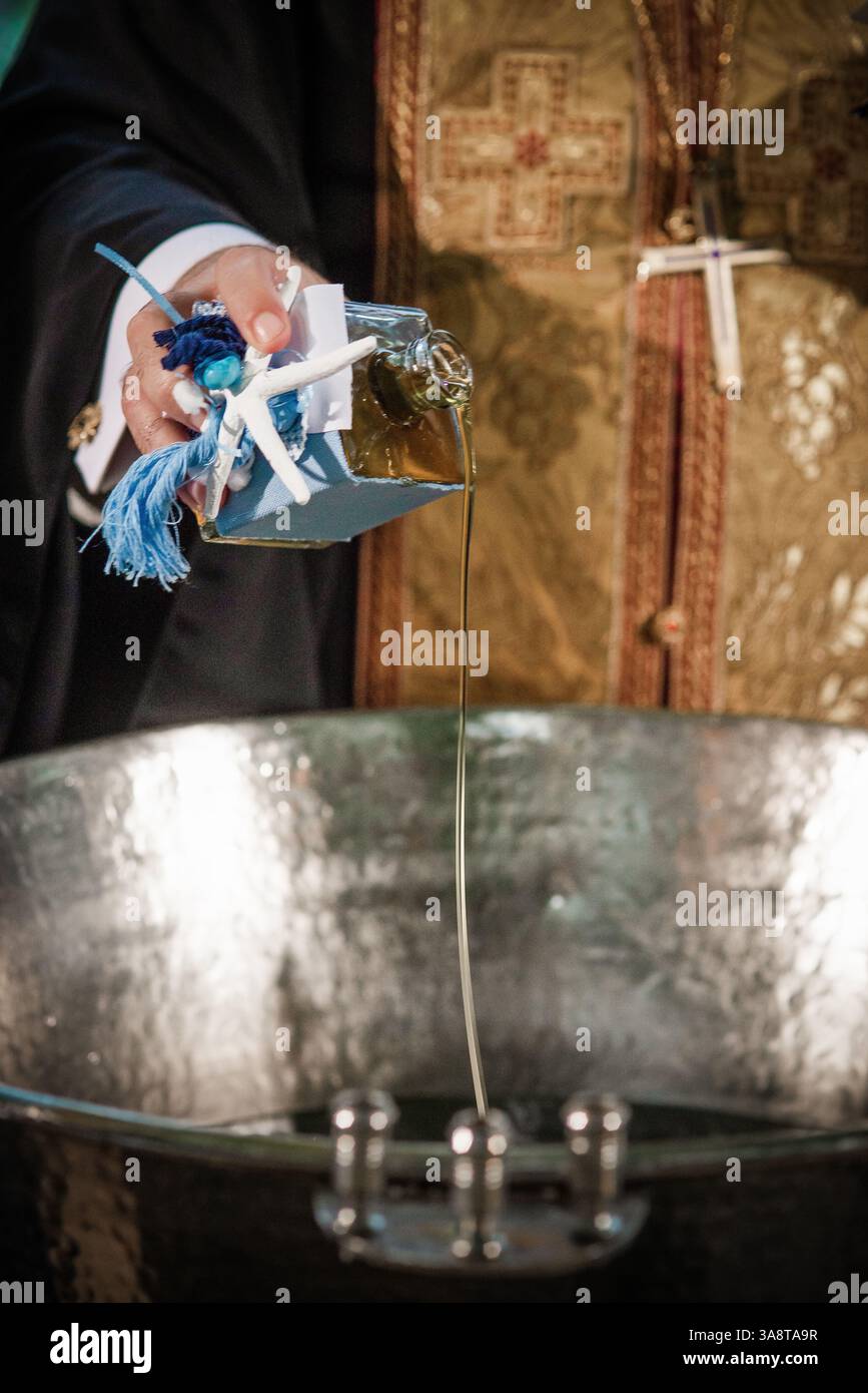 The priest pours olive oil in the font where the baby will be immersed ...