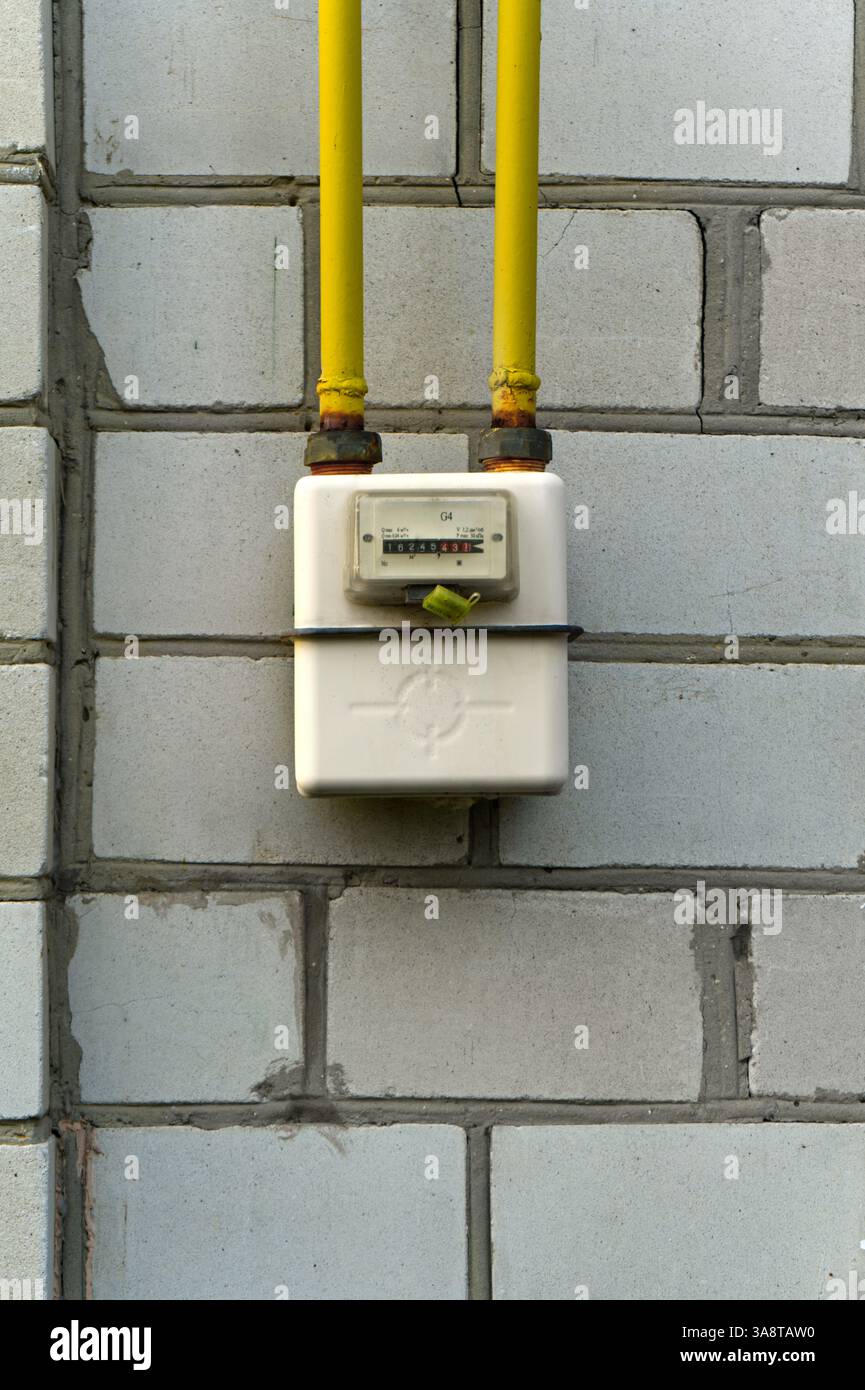 The image shows a gas meter attached to a grey brick wall with two ...