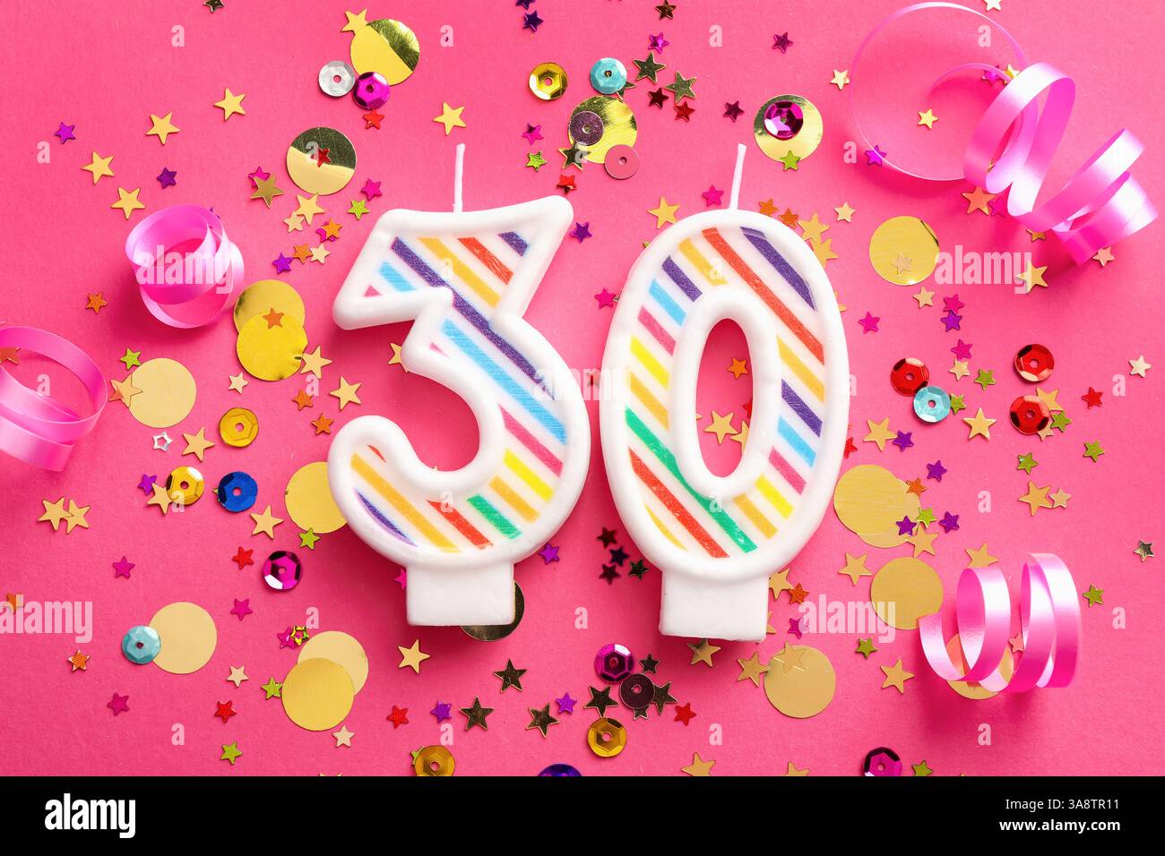30th birthday. Number shaped candles and confetti on pink background ...