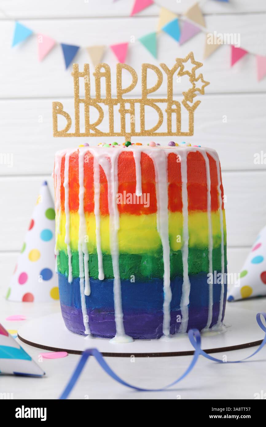 Delicious rainbow birthday cake with topper, party hats and confetti on ...
