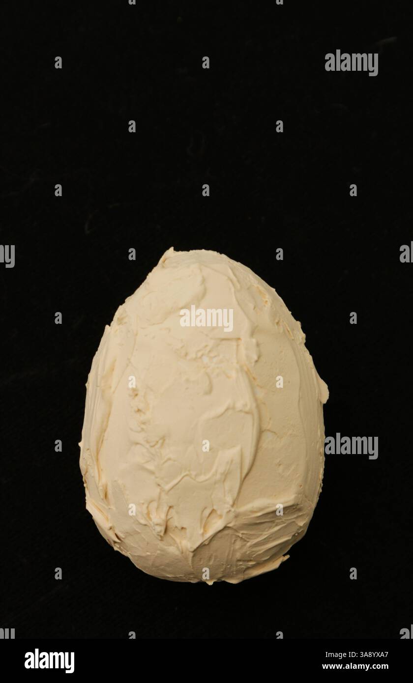 Vertical close-up photo of a plaster, rough homemade egg on a black background. Easter concept ...