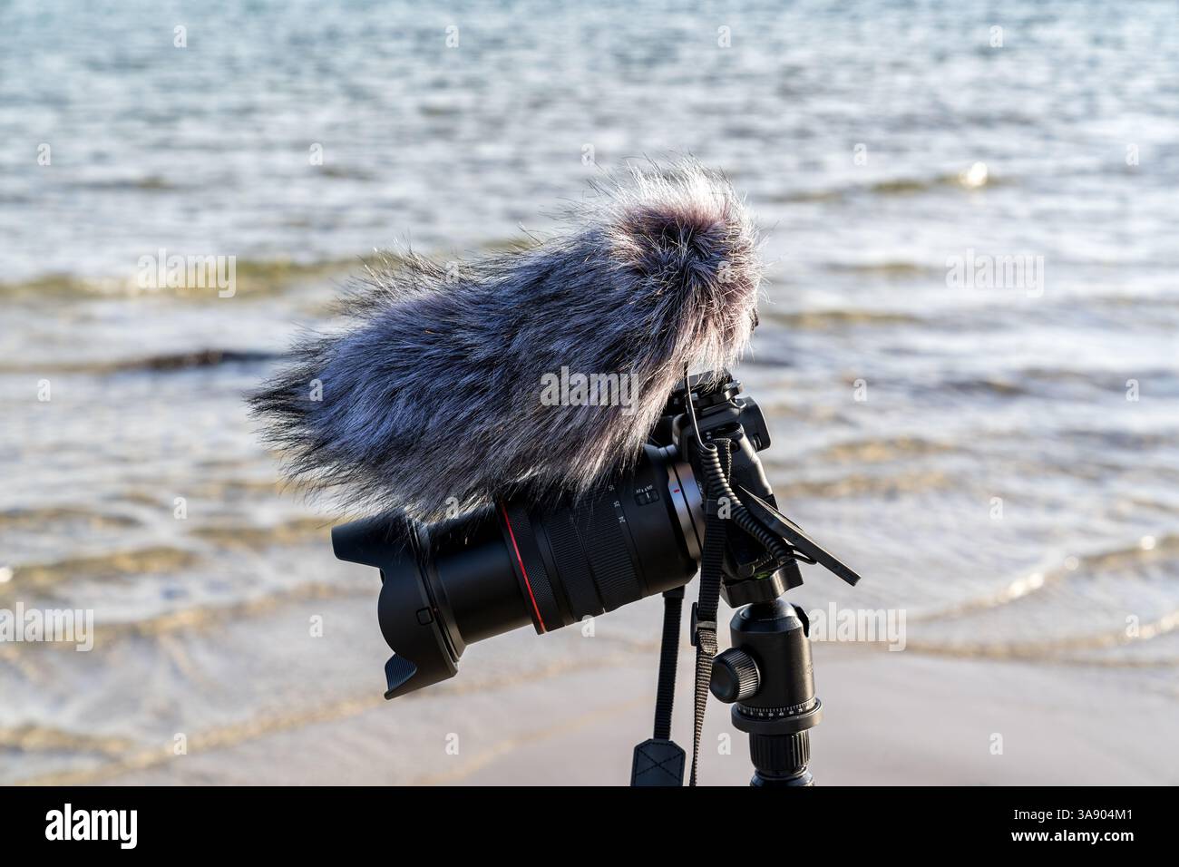 A camera is on a tripod on a beach. The camera is recording the ocean ...