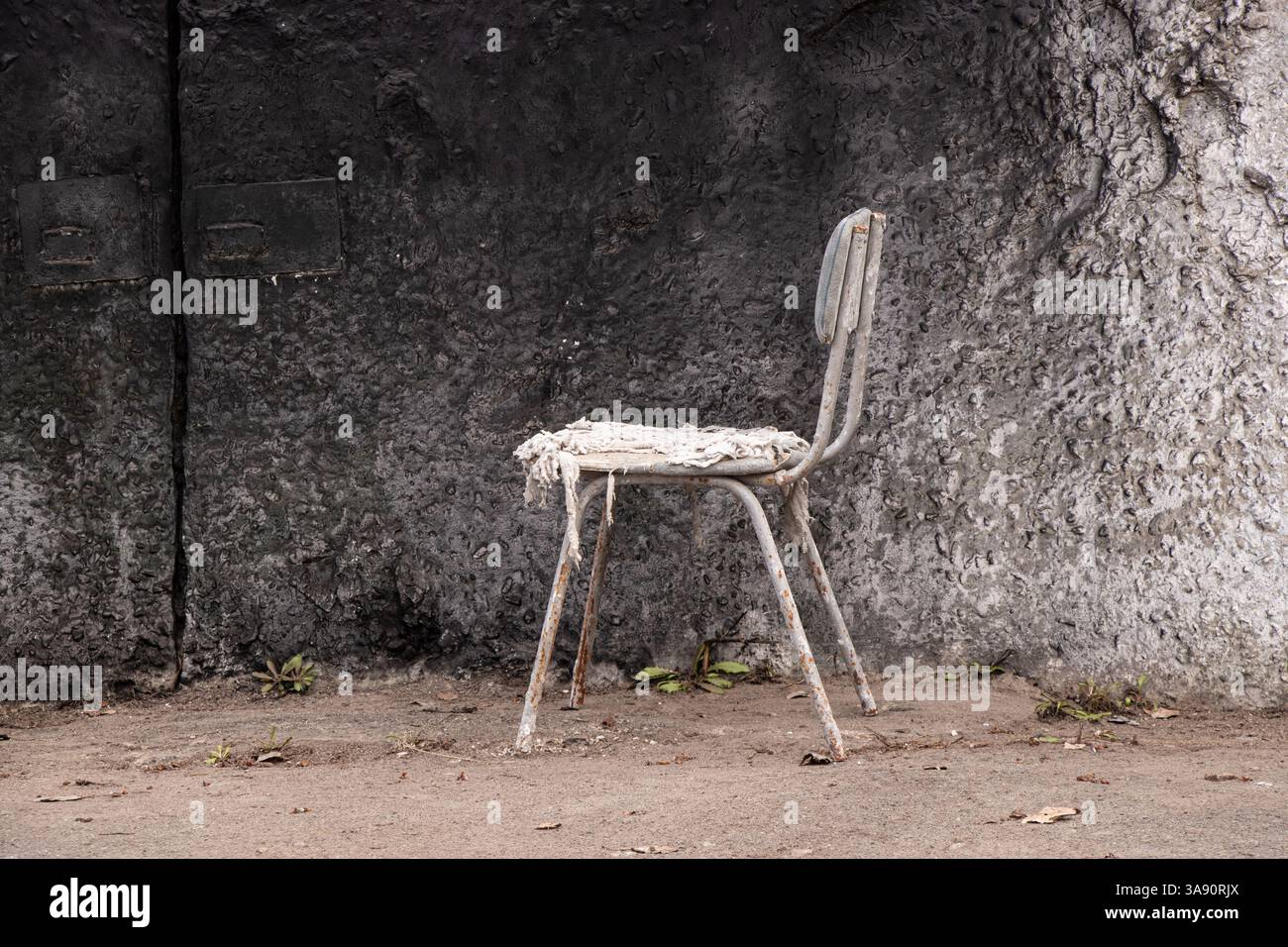 Old dirty torn chair stands near concrete black wall as a place to rest ...