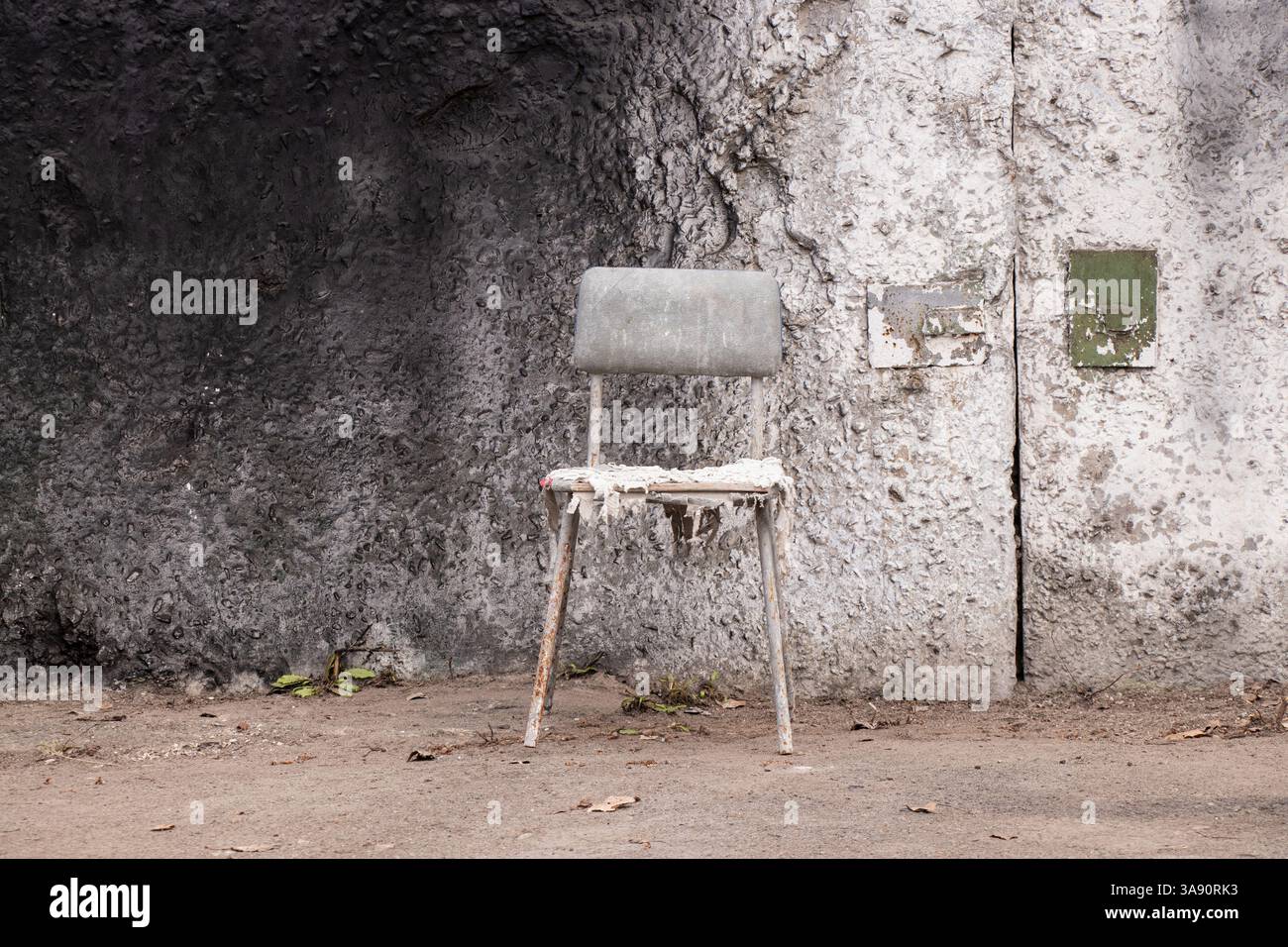 Old dirty torn chair stands near concrete black wall as a place to rest ...