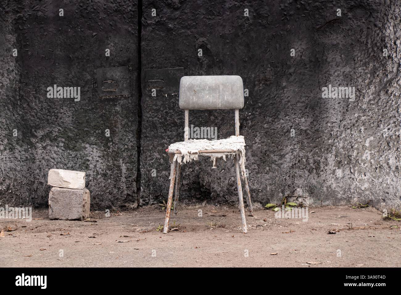 Old dirty torn chair stands near concrete black wall as a place to rest ...