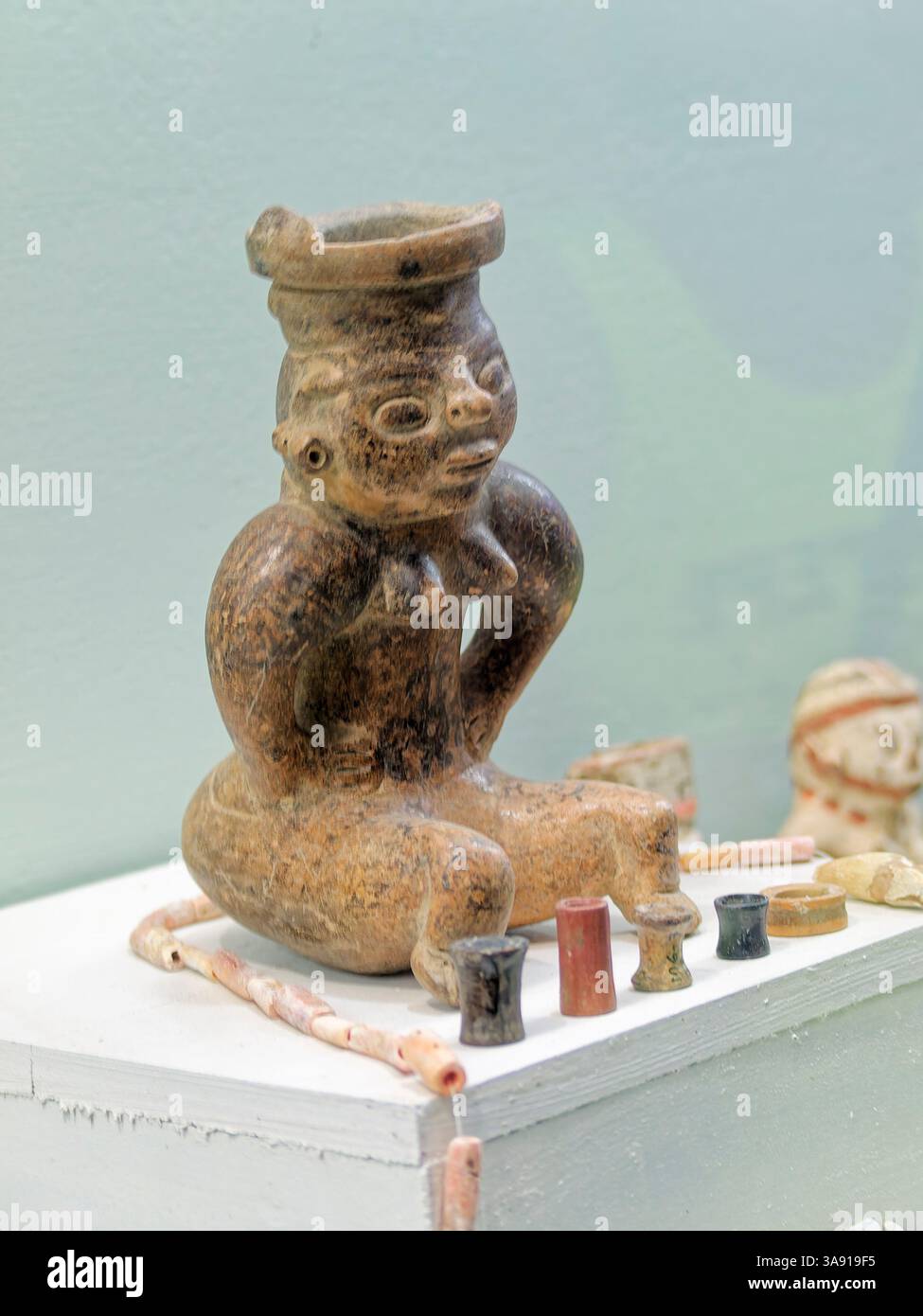 Pottery jug in shape of seated person. Ear plugs in various colors and ...