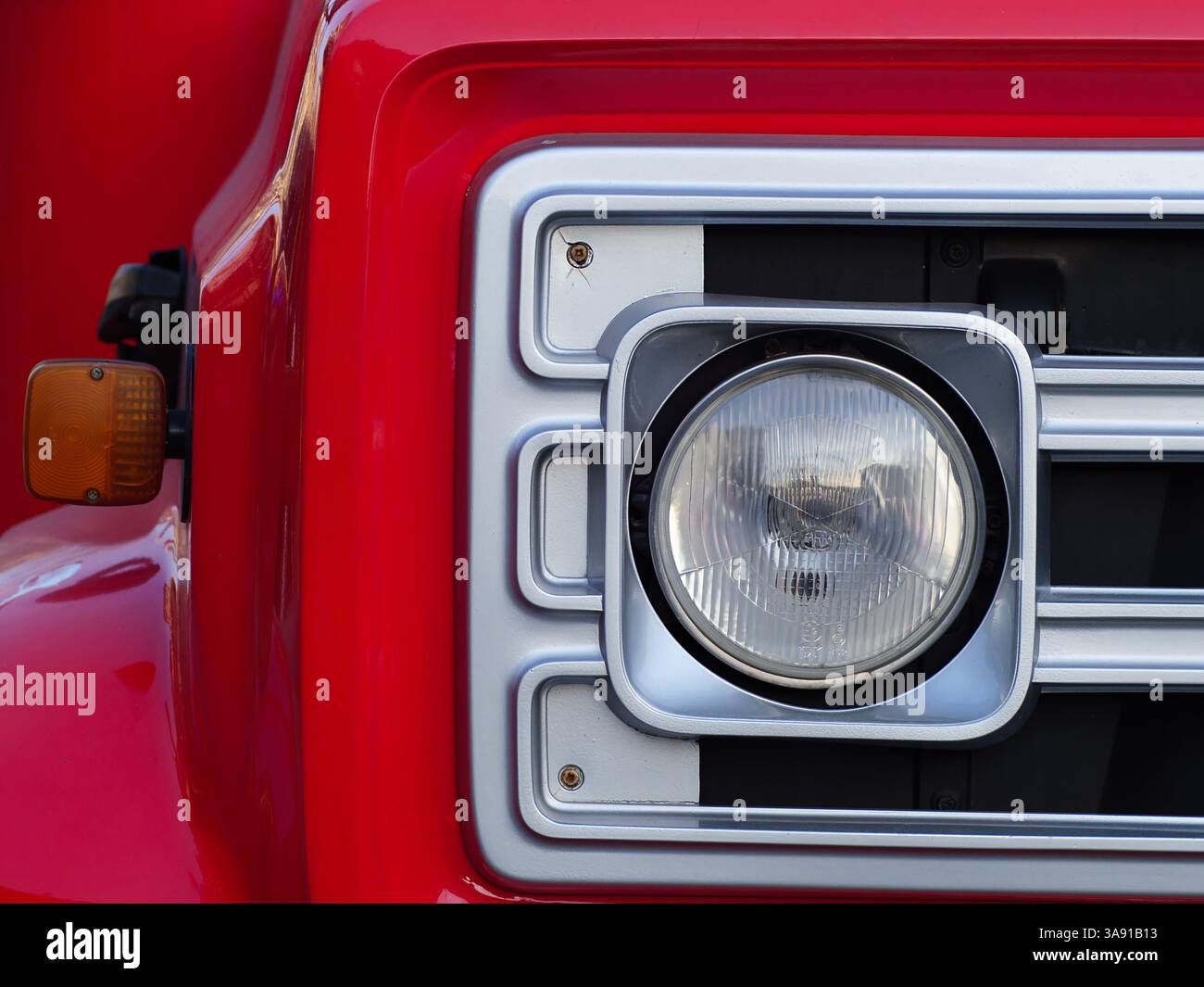 A detailed close-up photograph of the headlight on a red GMC Bluebird ...