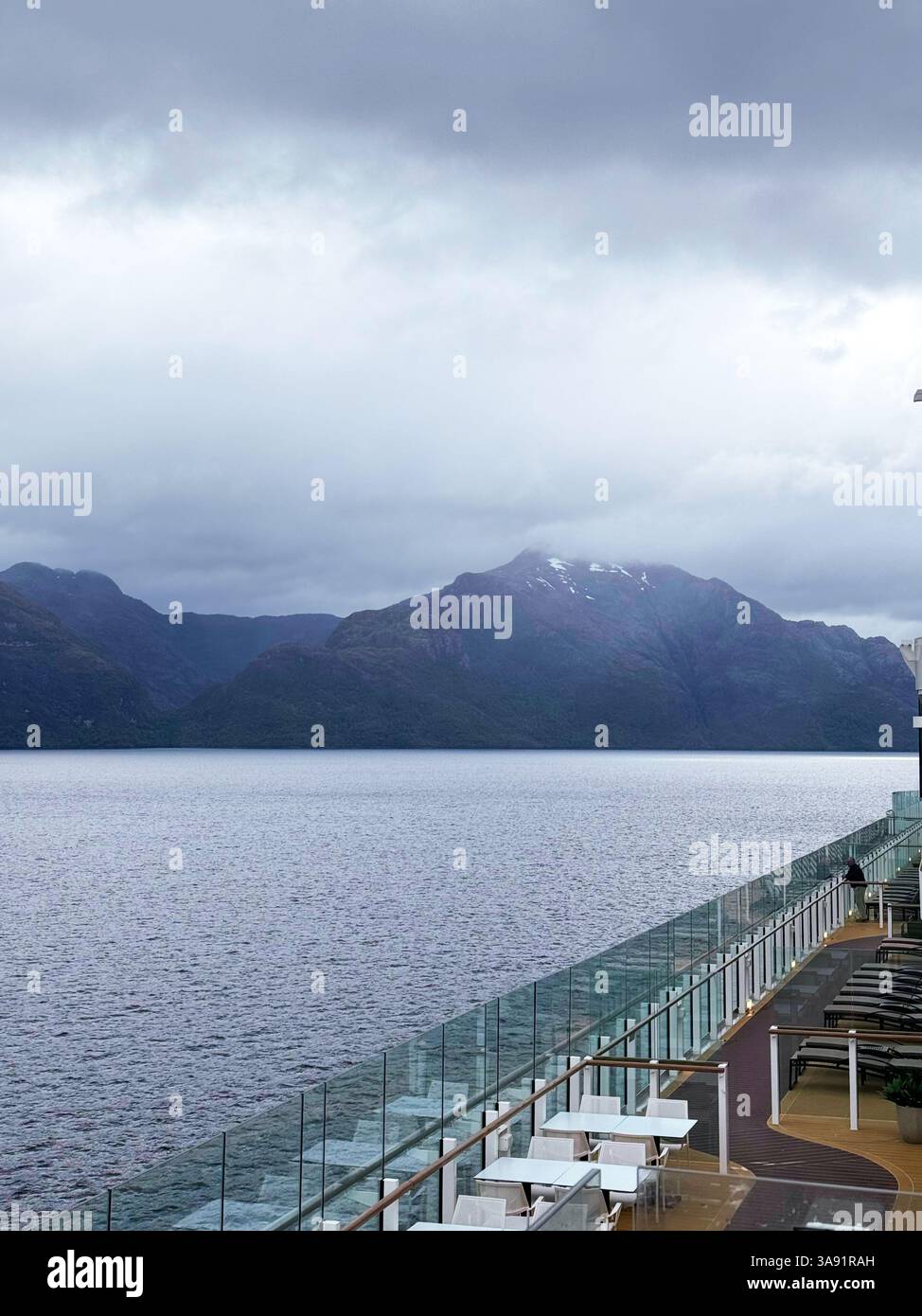 A peaceful cruise ship deck with empty lounge chairs and tables faces a ...