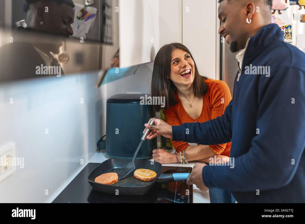 Cheerful multiethnic couple laughing and having fun while preparing ...