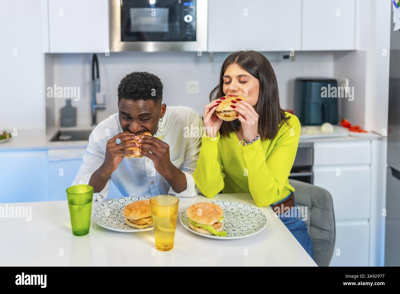 Young multiethnic couple eating homemade burgers in their modern ...