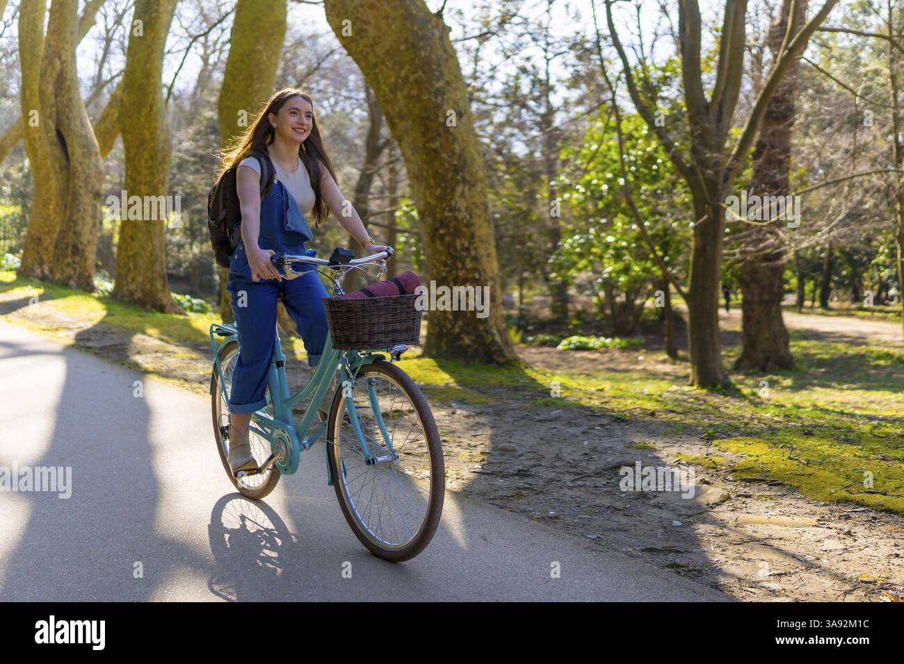 Young woman riding a vintage bicycle through a sunlit park, enjoying ...