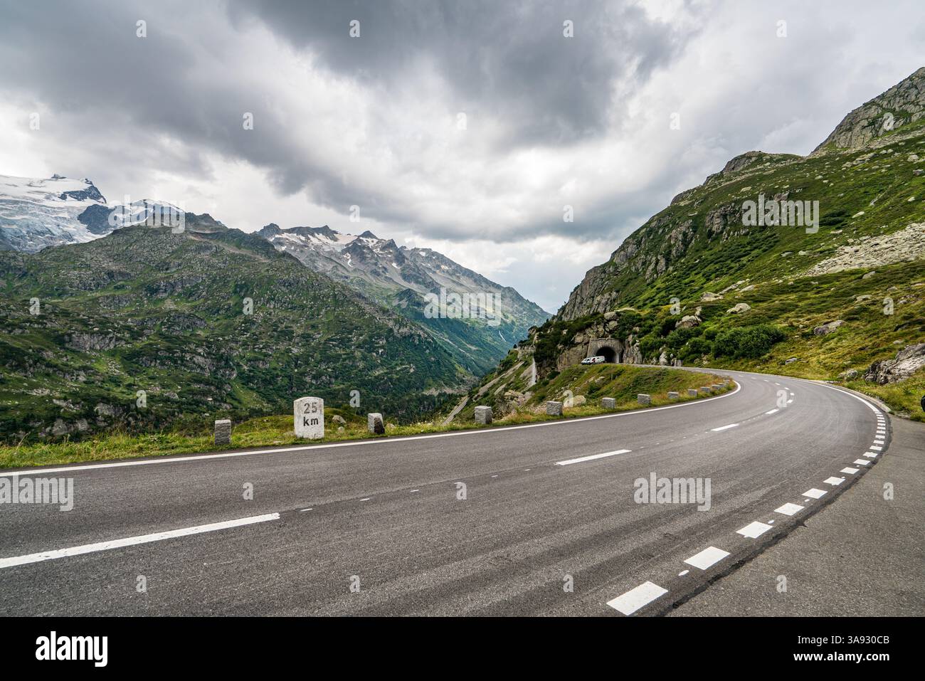 A road in Swiss Alps with a white line down the middle. The road is ...
