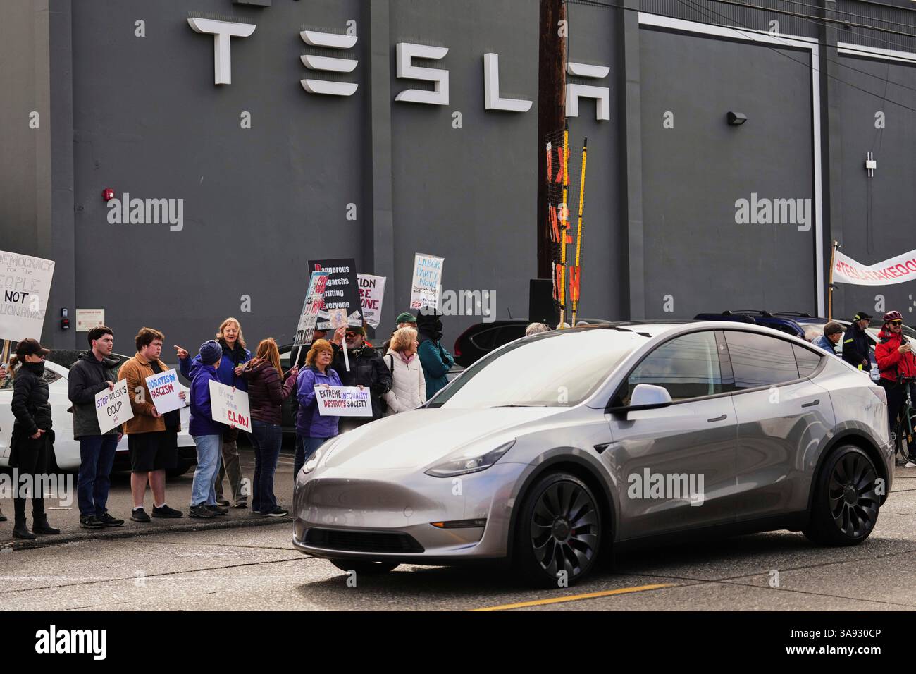 A driver in a Tesla passes by people gathered to protest Elon Musk and ...