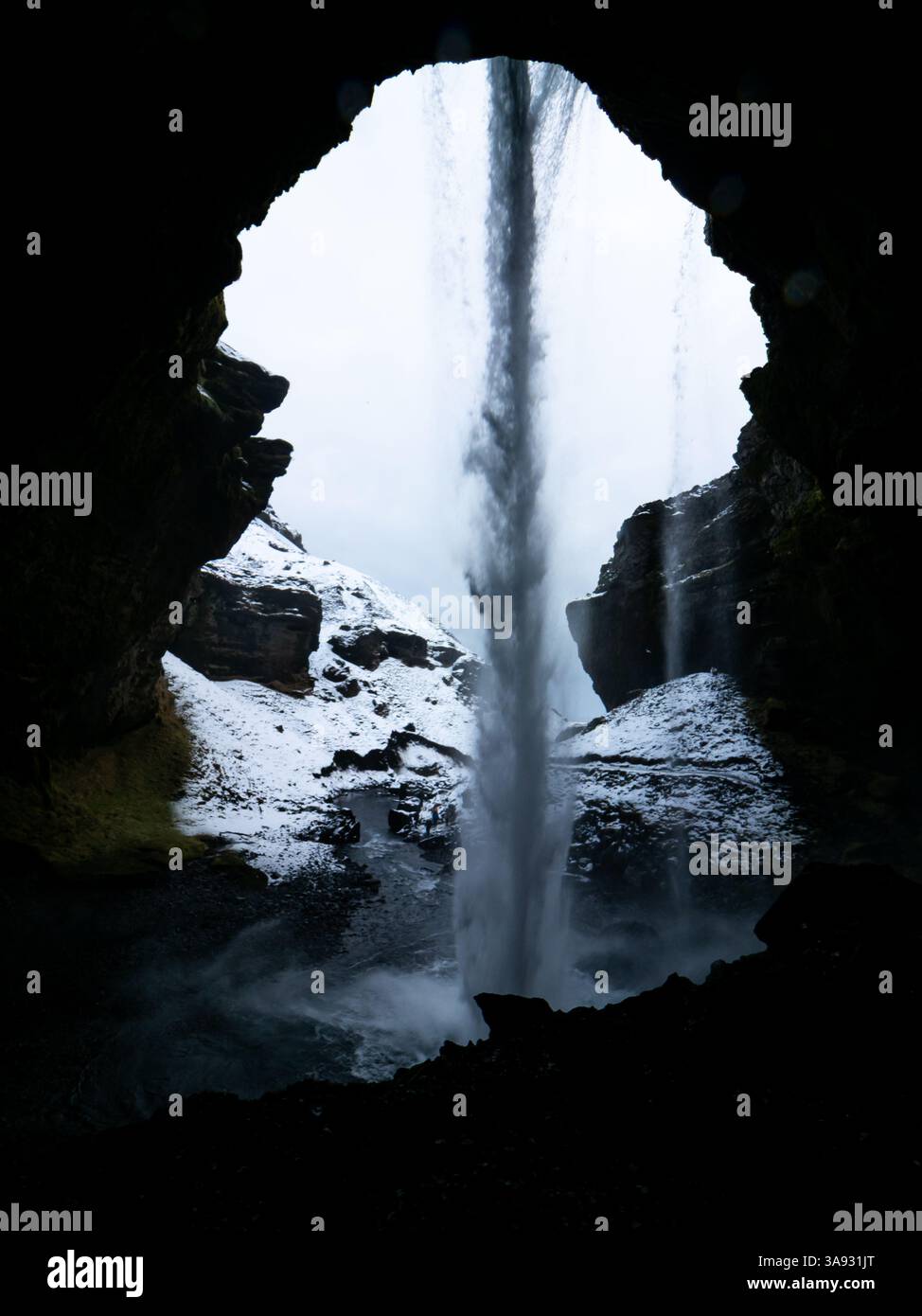 Kvernufoss waterfall as seen from behind, framed by a dark cave opening ...