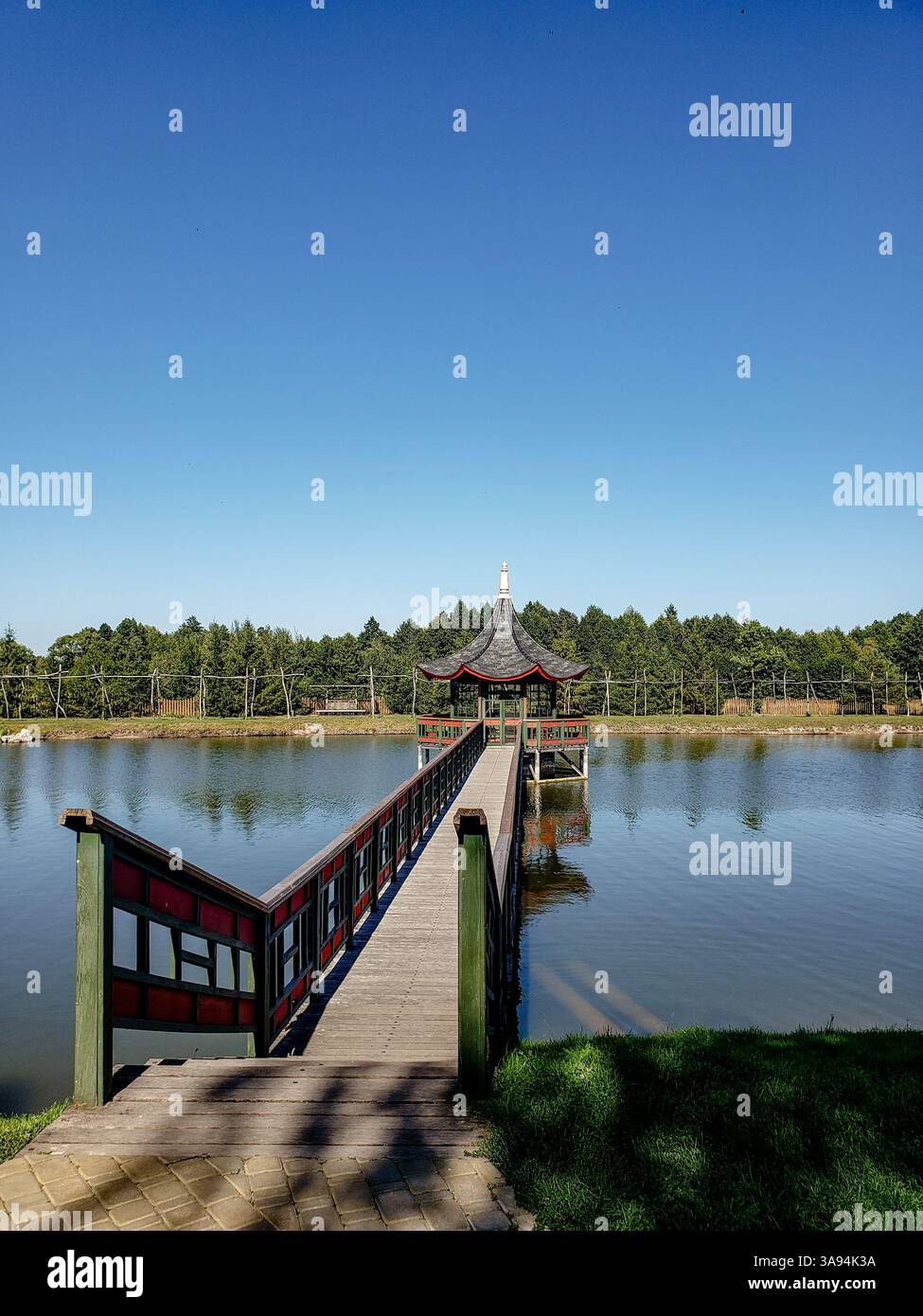 Traditional Chinese pavilion with red railings on a wooden bridge over ...