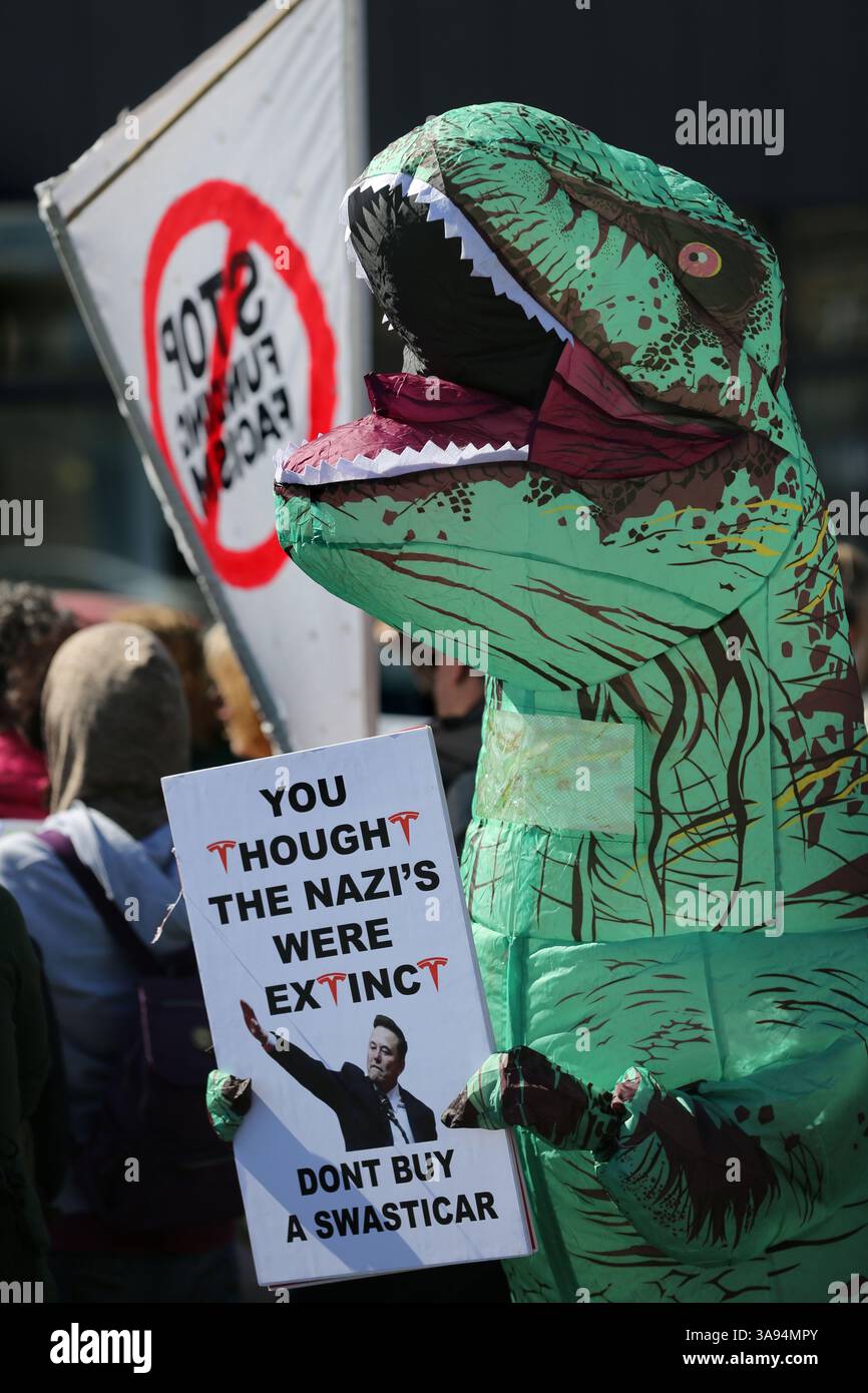 A protester in a t-rex dinosaur suit holds a placard saying ‘You ...
