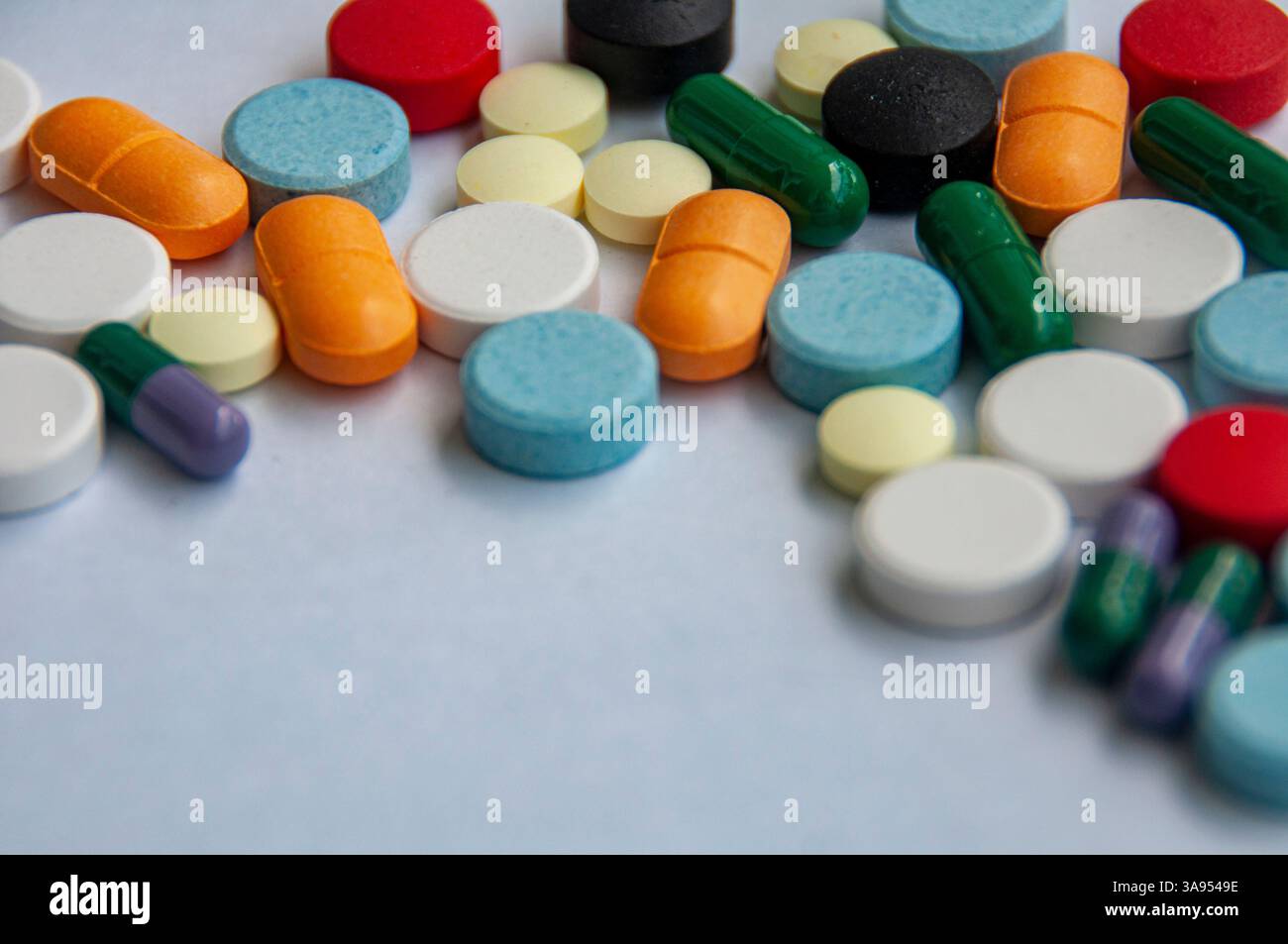 Colorful pills and capsules scattered on a light colored surface with ...