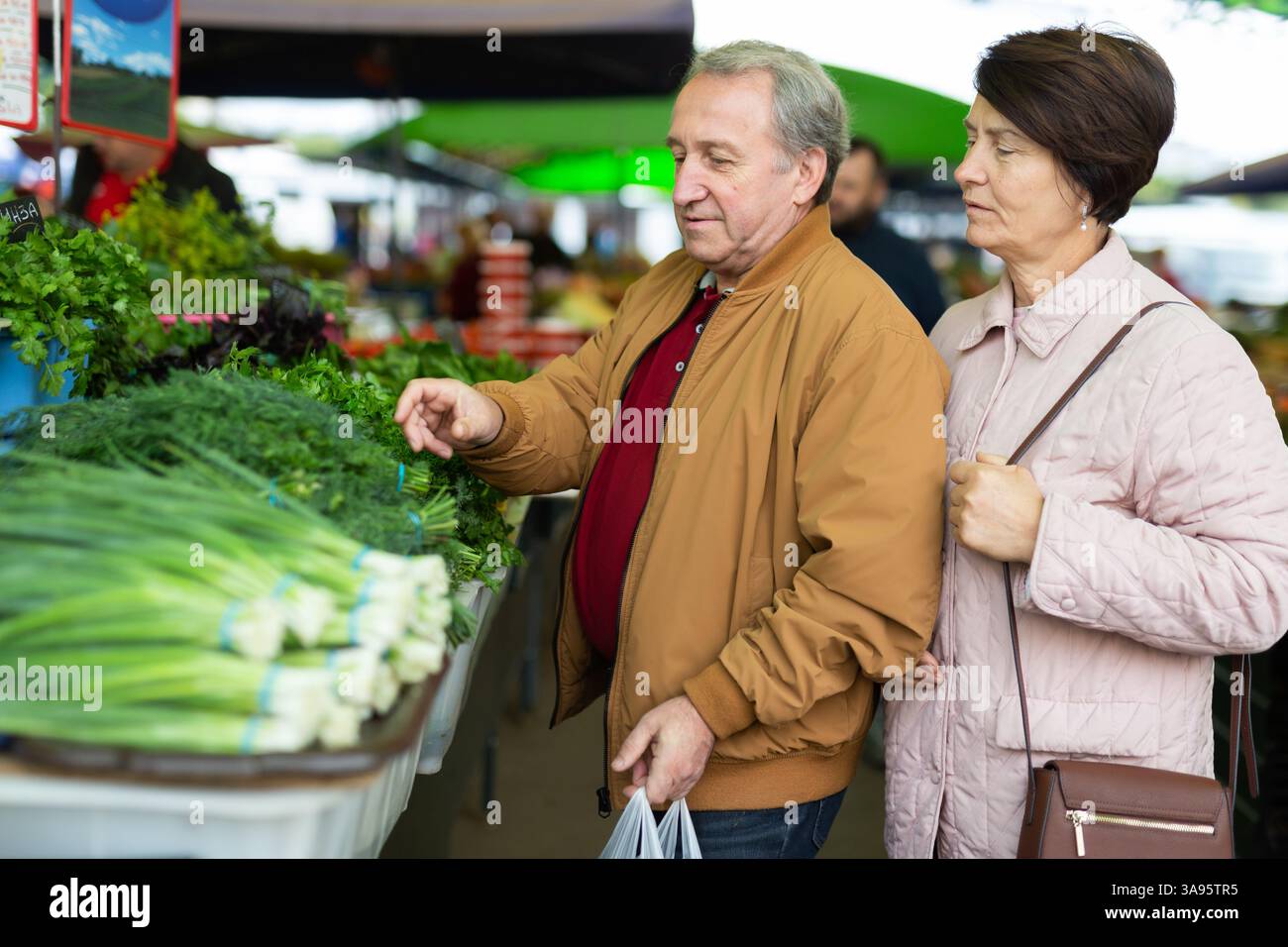 Positive mature male and female picking dill at local grocery bazaar ...