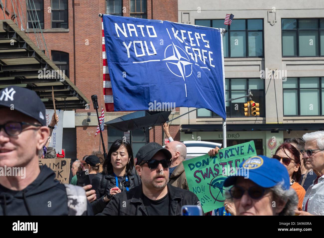 A protester holds a NATO flags that says "NATO KEEPS YOU SAFE" during a ...