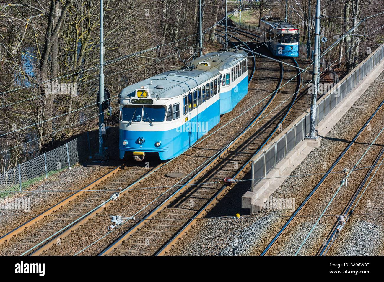 Trams navigate the tracks in Gothenburg during spring, showcasing vibrant greenery along the ...
