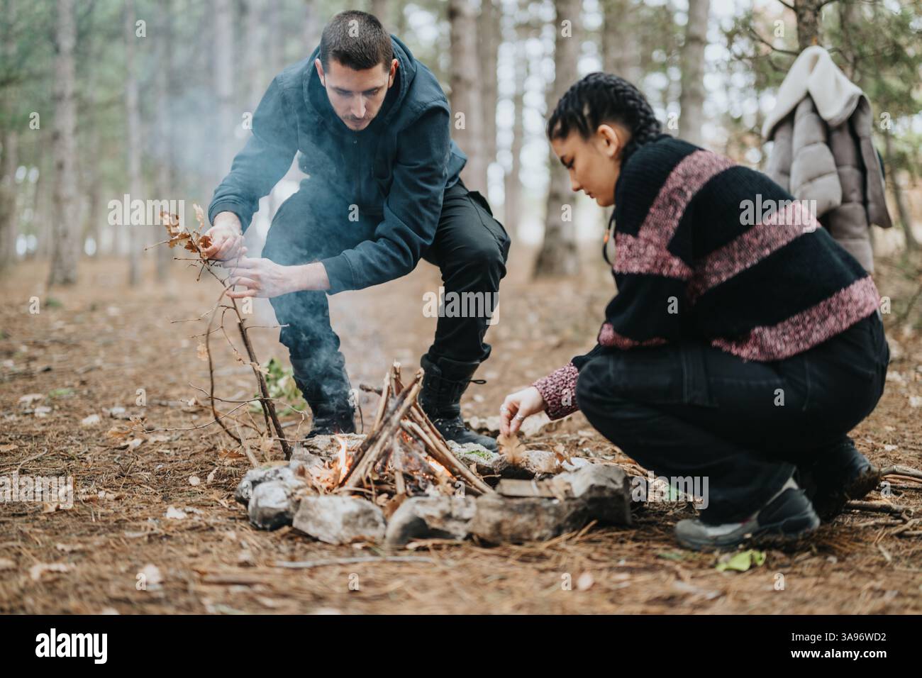 Two individuals building a campfire in a forest setting surrounded by ...
