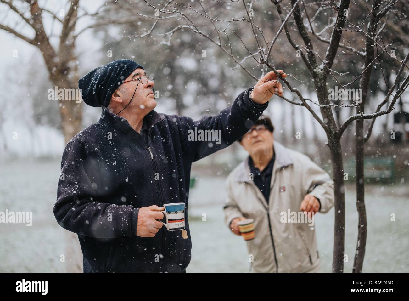 Two senior men enjoying snow outside, drinking hot beverages and ...