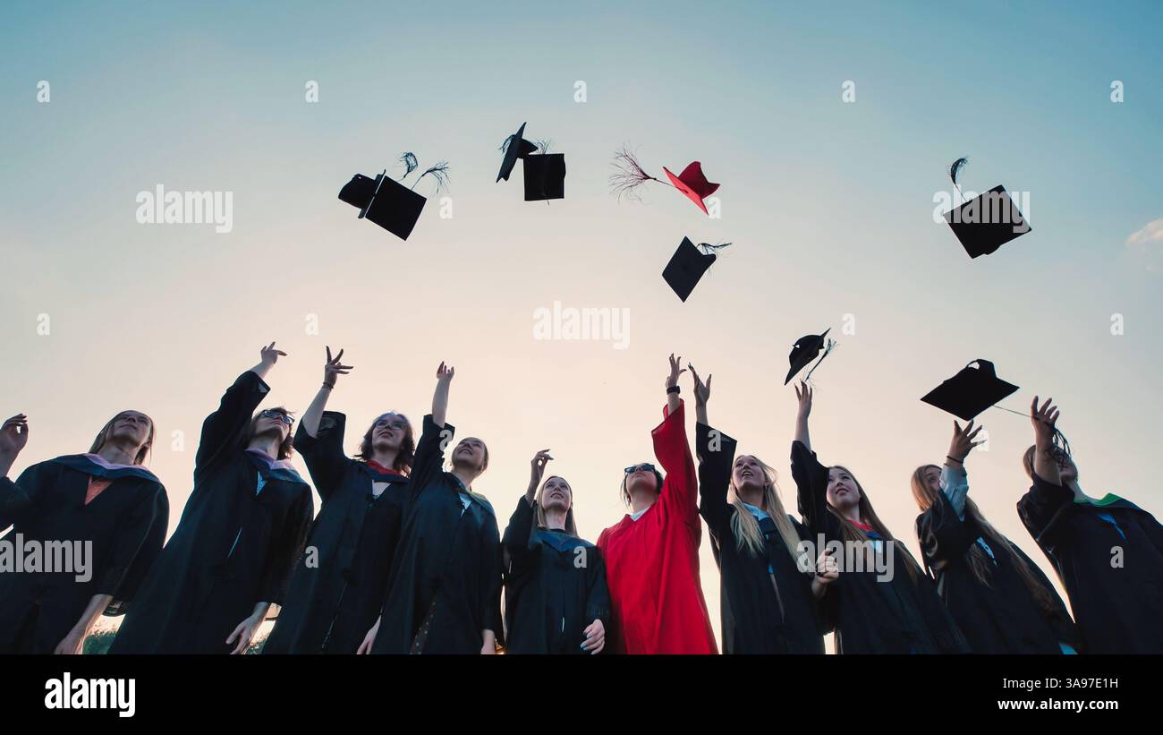 Happy students in academic gowns tossing graduation caps in the air to ...