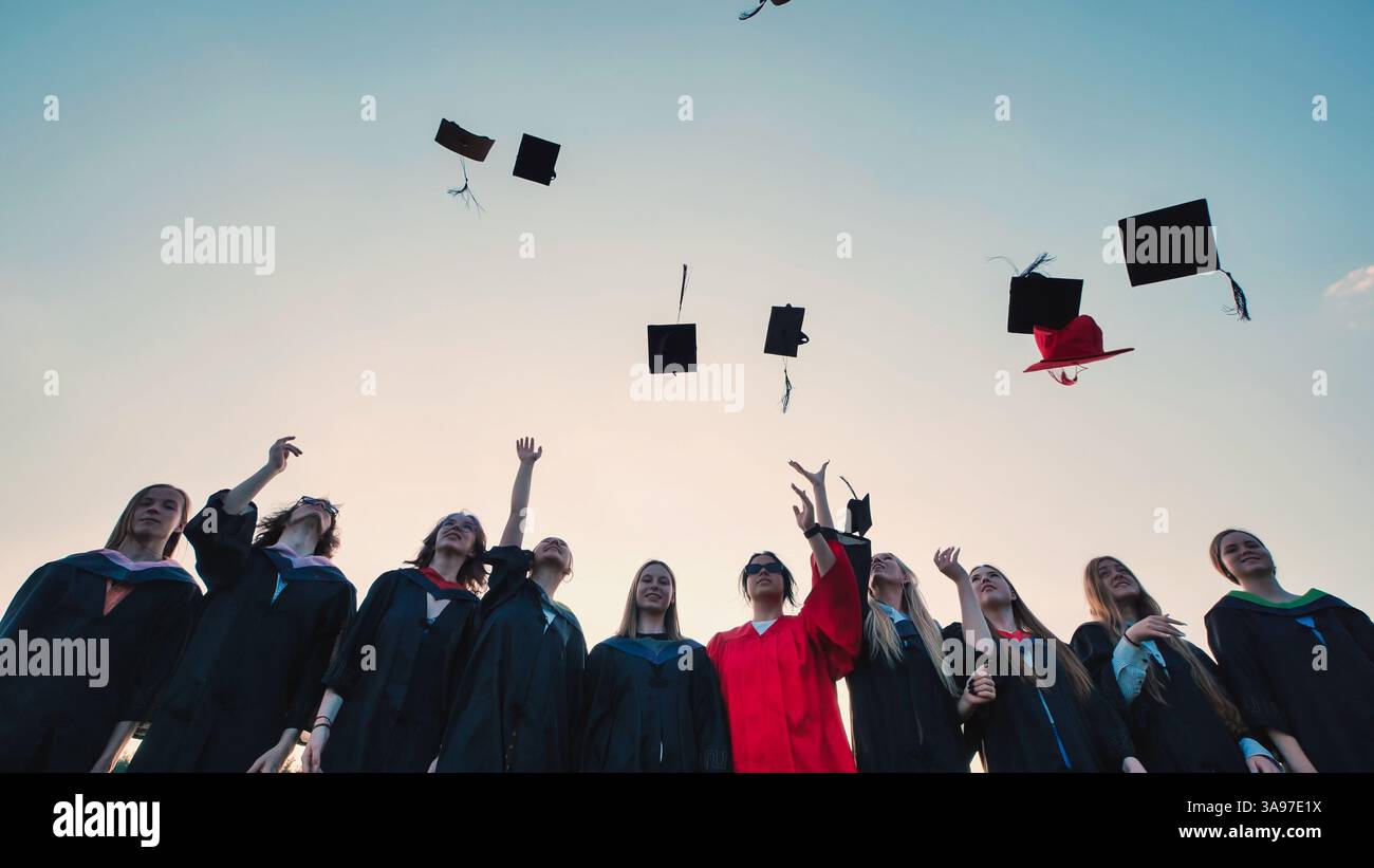 Happy students in graduation gowns tossing caps in the air to celebrate ...