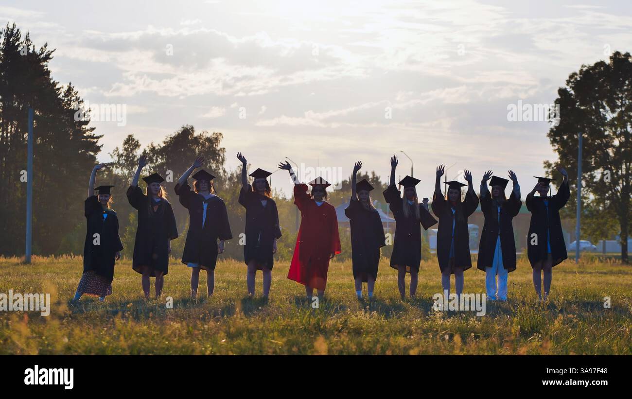 Group of joyful graduates in academic gowns raising hands in ...
