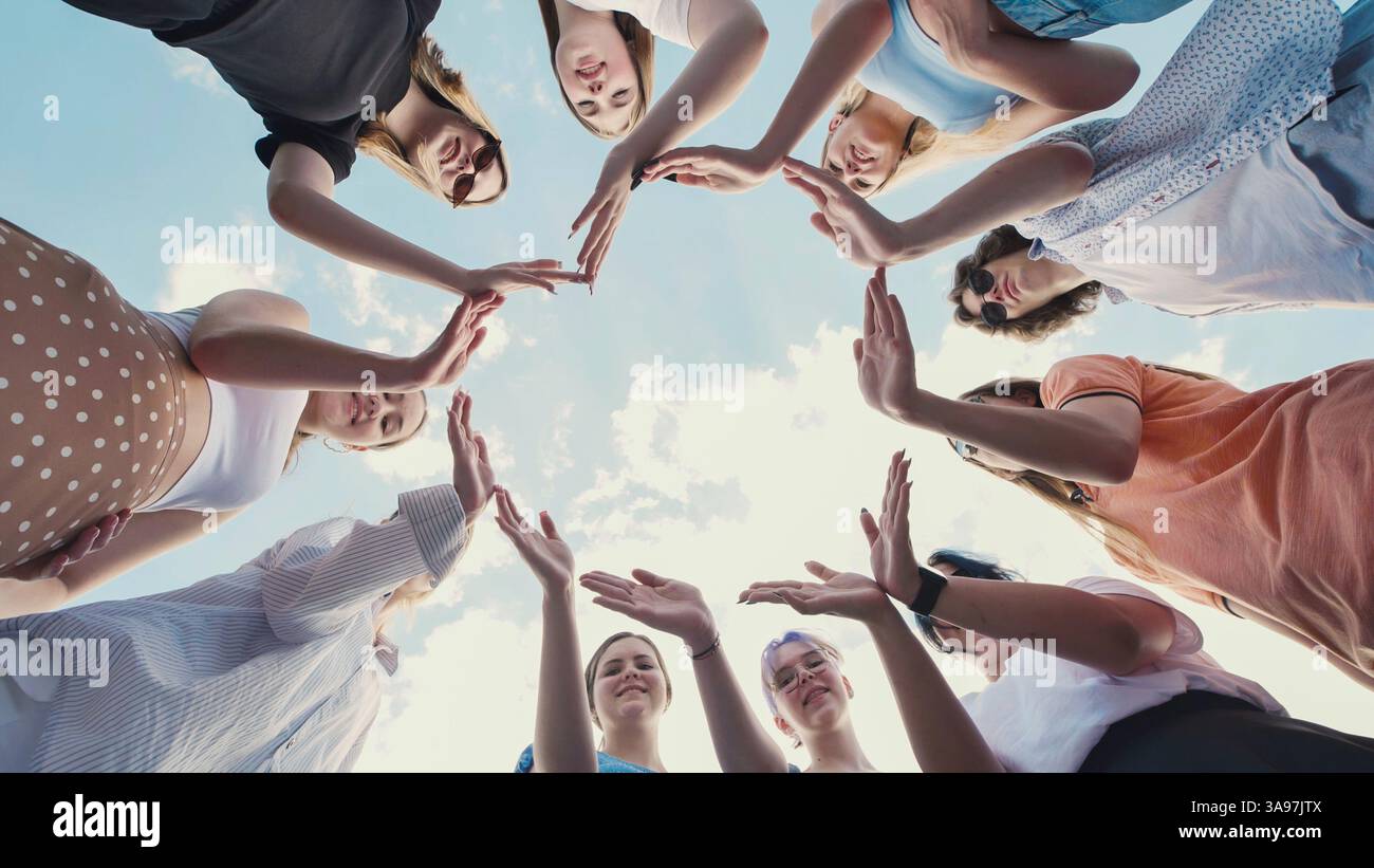 Group of students making a circle with their hands against a blue sky ...