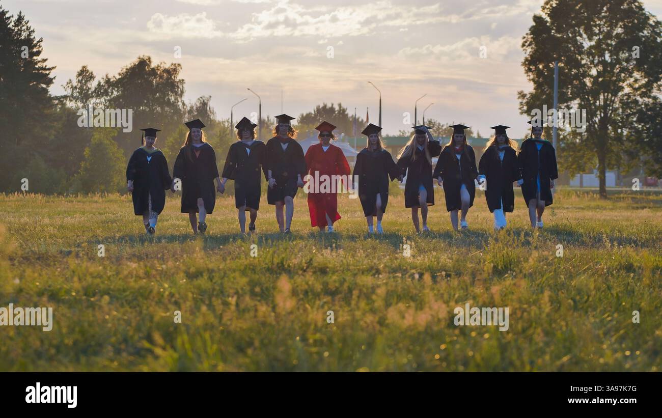 Graduating students in cap and gown walking together in a field at ...