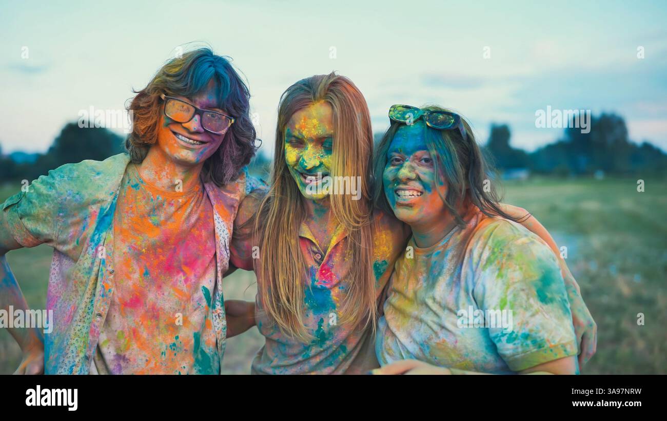 Three happy school buddies, adorned in colorful holi powder, hug and ...