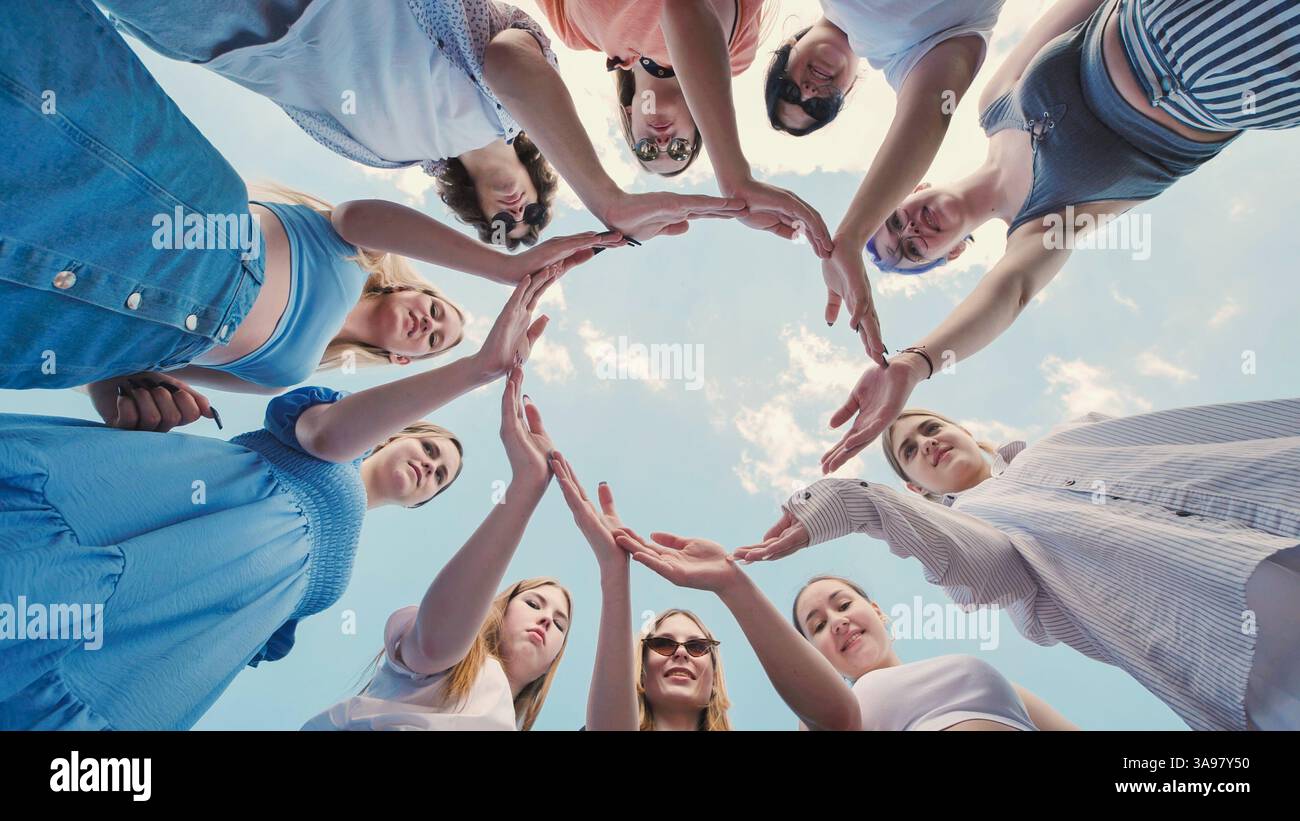 School friends joining hands in a circle under a clear blue sky ...