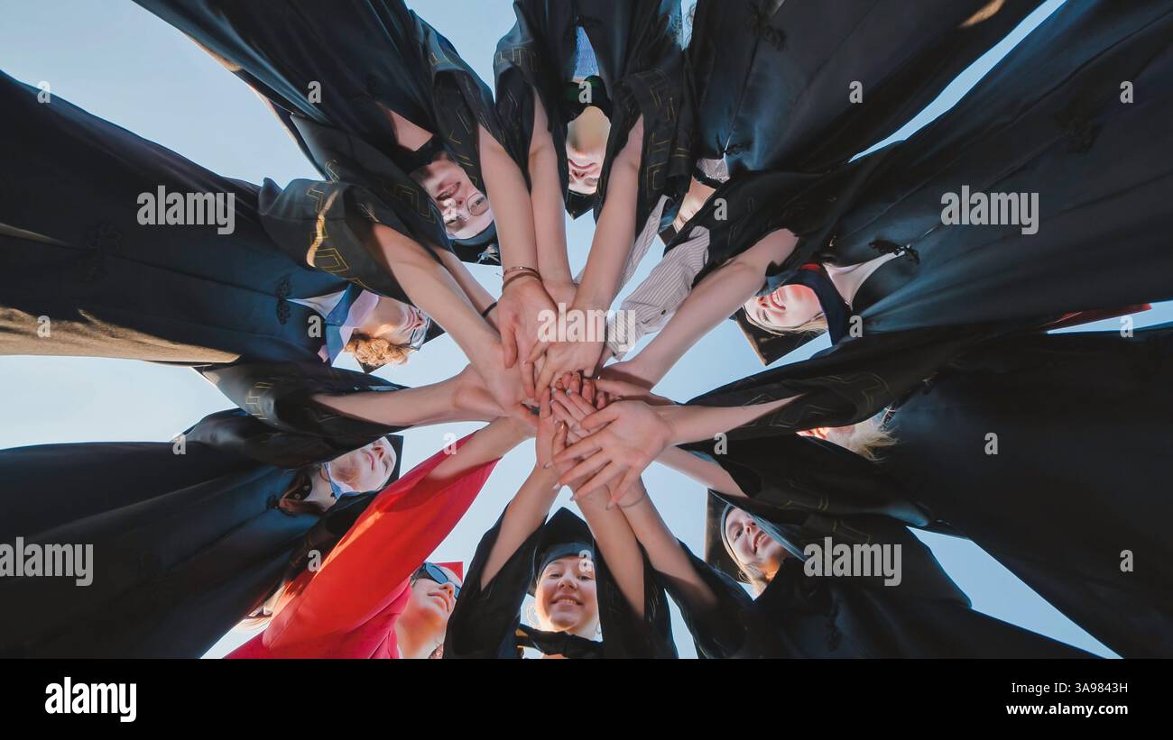 Smiling graduates in academic gowns join hands in unity, celebrating ...