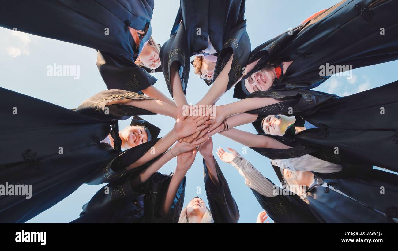 Cheerful graduates in academic gowns joyfully celebrate their ...