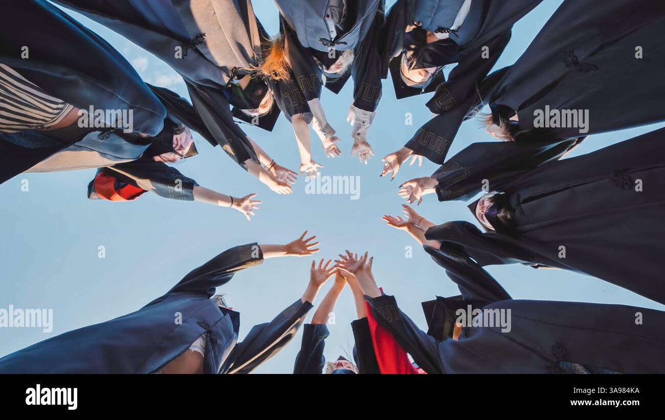 Group of students in graduation attire holding hands in a circle ...