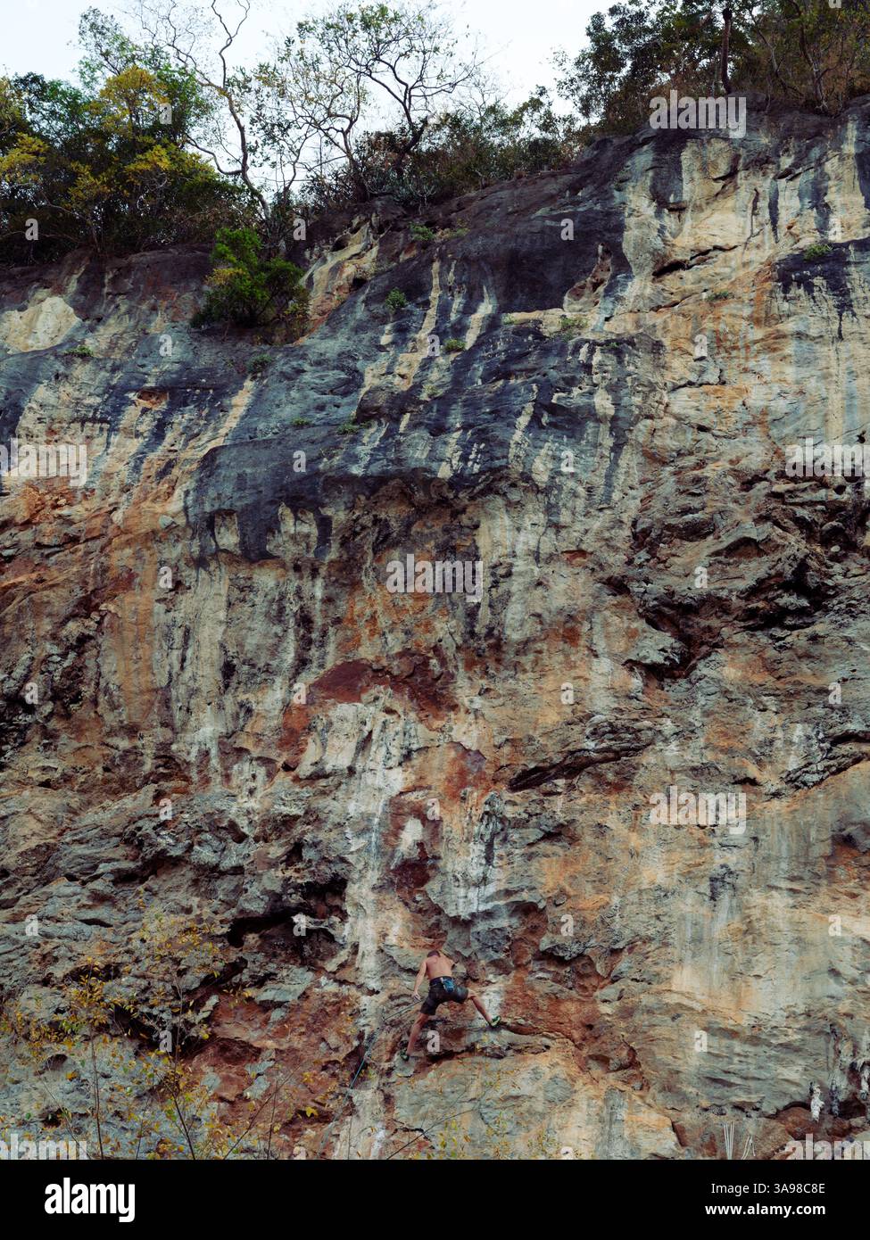 Climber scales a cliff streaked with mineral hues and natural textures, dwarfed by the vertical ...