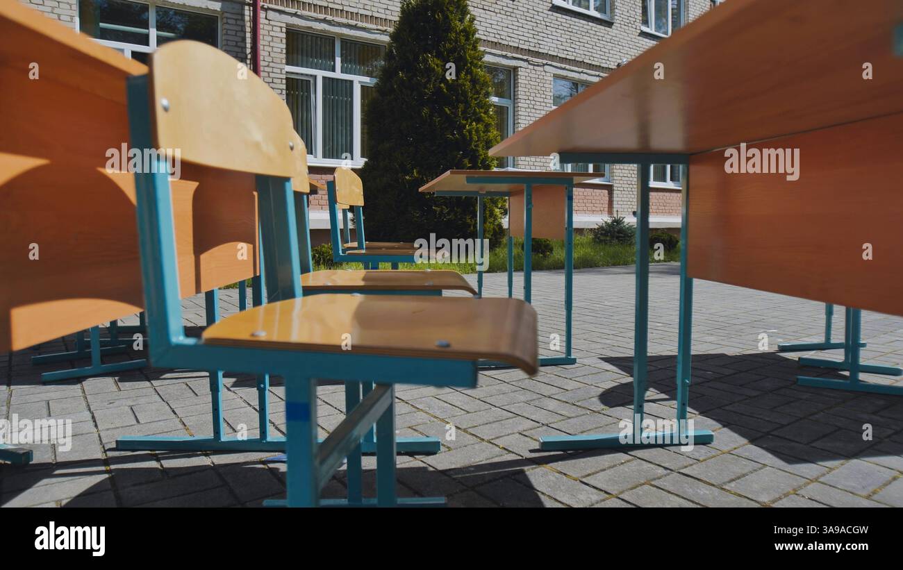 Empty desks and chairs stand outside a school building, suggesting an ...