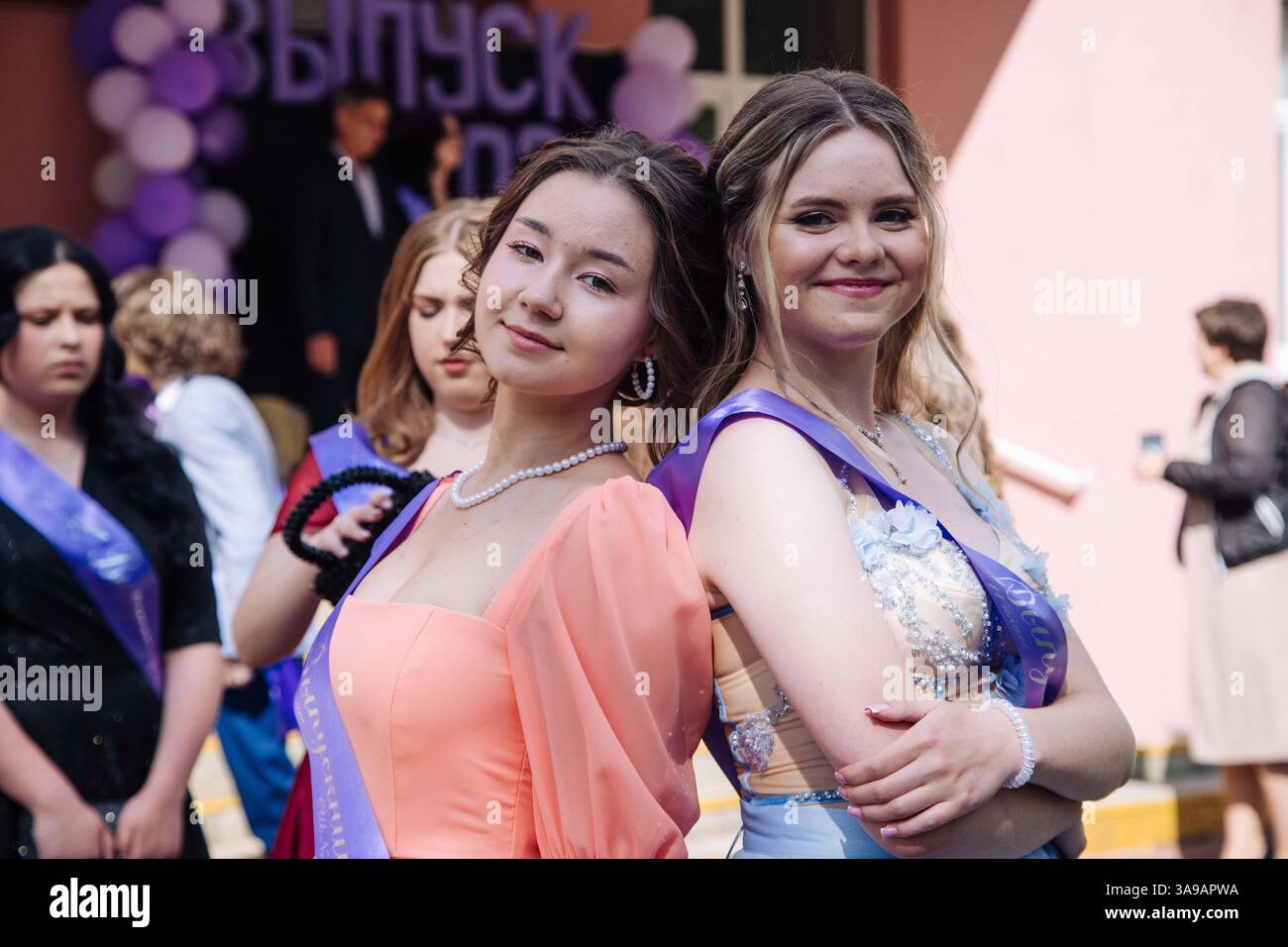 Female graduates wearing colorful sashes standing together, smiling and ...