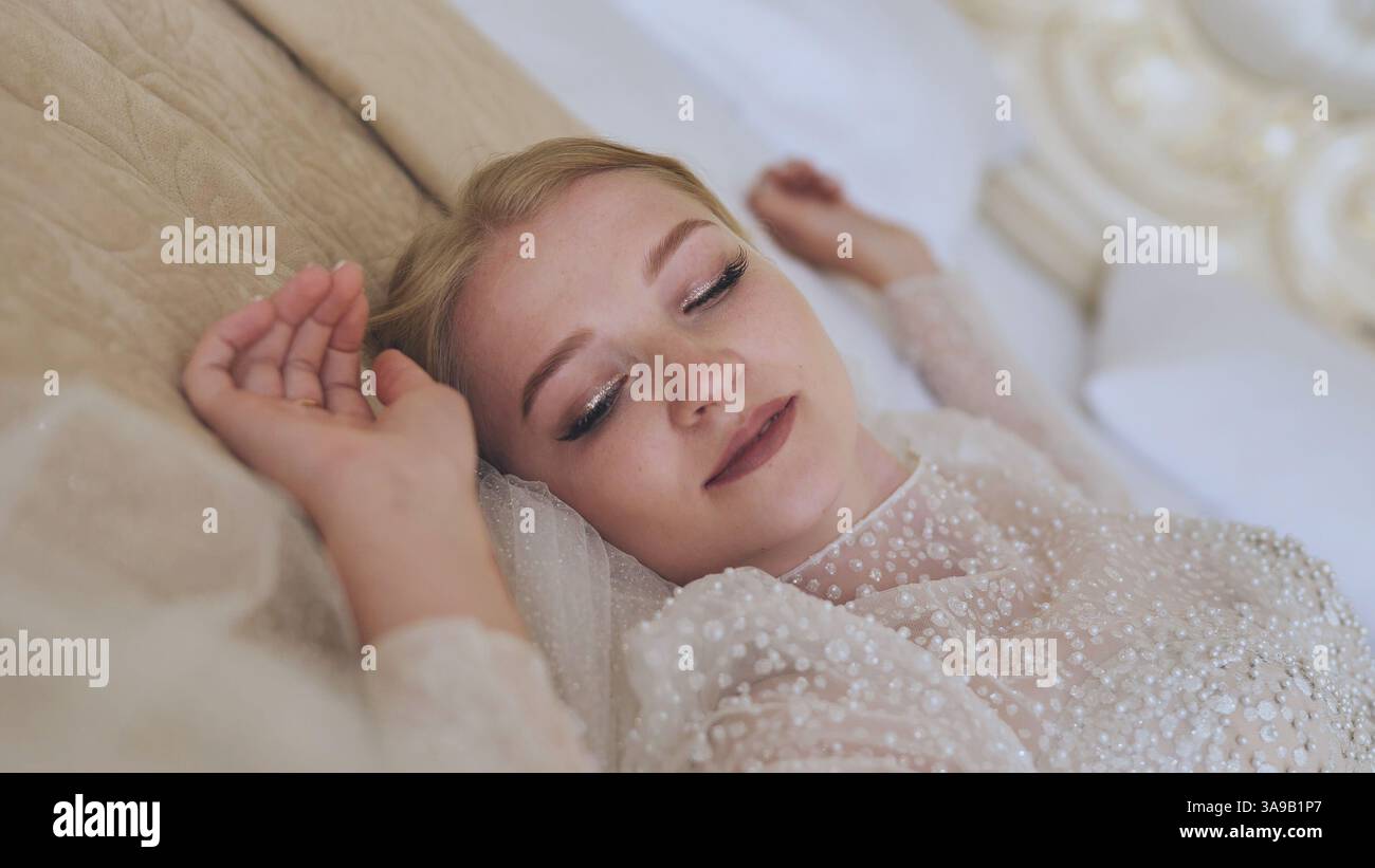 Elegant bride relaxing on bed, wearing white wedding gown with pearl ...