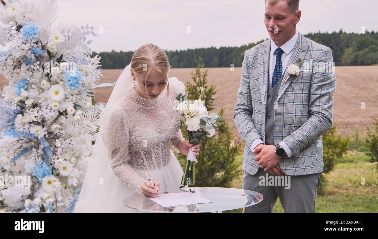 Bride signing marriage certificate during outdoor wedding ceremony with ...