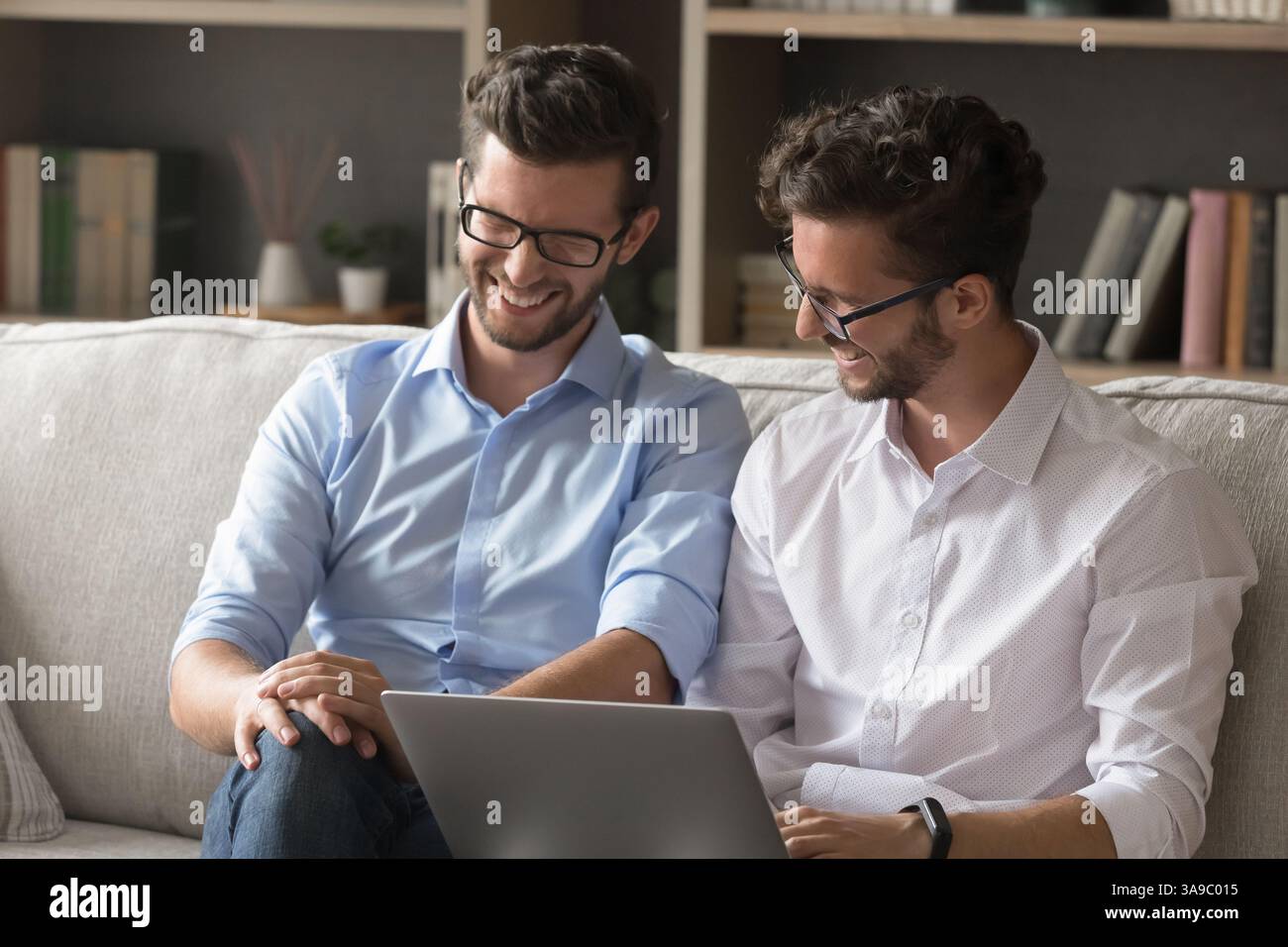 Laughing gen z twin brothers relaxing on sofa using notebook Stock ...