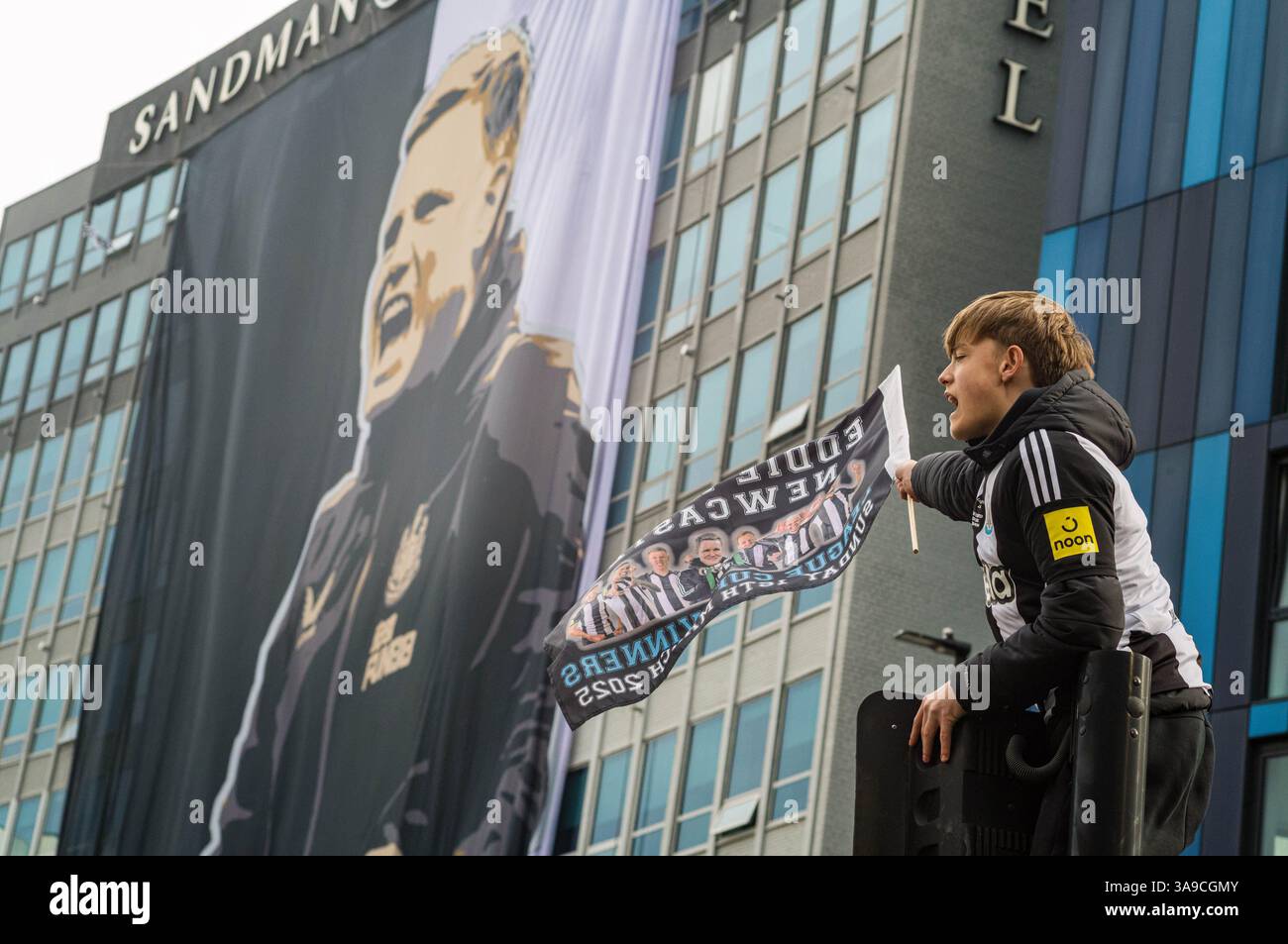 A young Newcastle United fan waves a flag in front of a huge banner of ...
