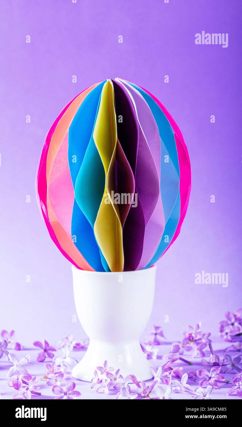 Decorative paper Easter egg in an egg cup and lilac flowers on a lilac ...