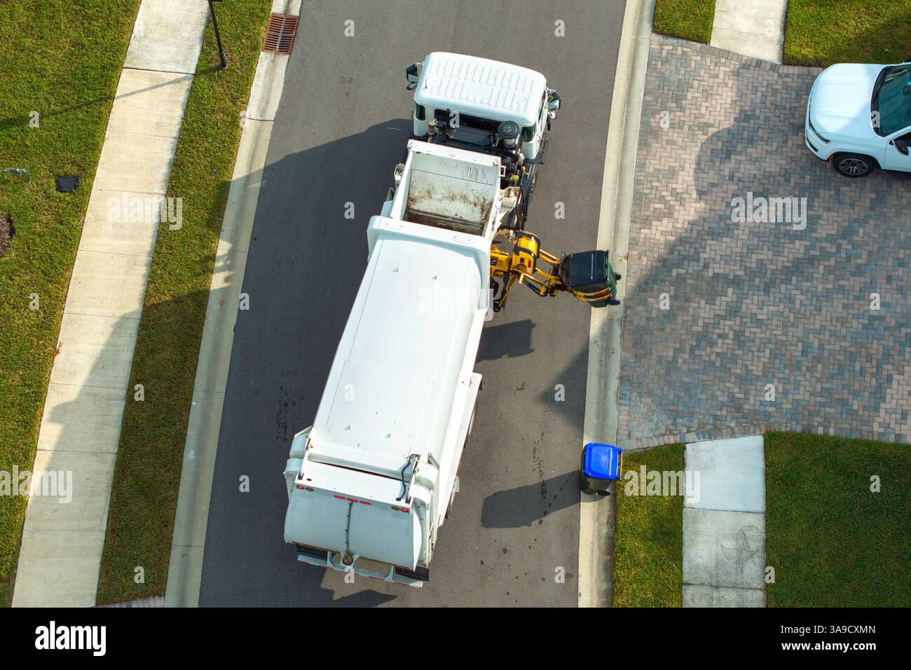 Garbage truck loading trash bin from the curb of American neighborhood ...